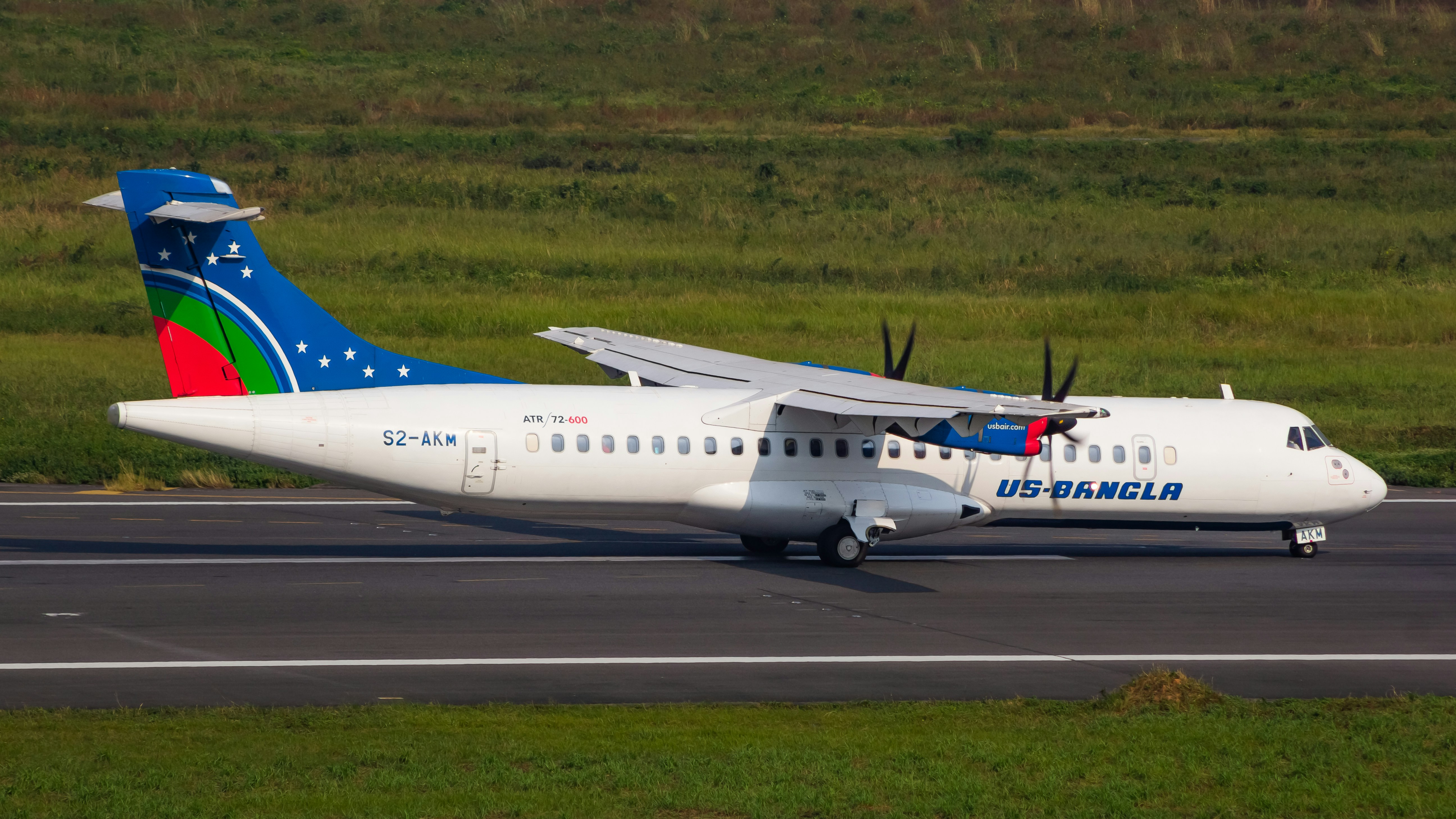 US-Bangla Airlines ATR aircraft preparing for takeoff on a vibrant runway surrounded by lush greenery.