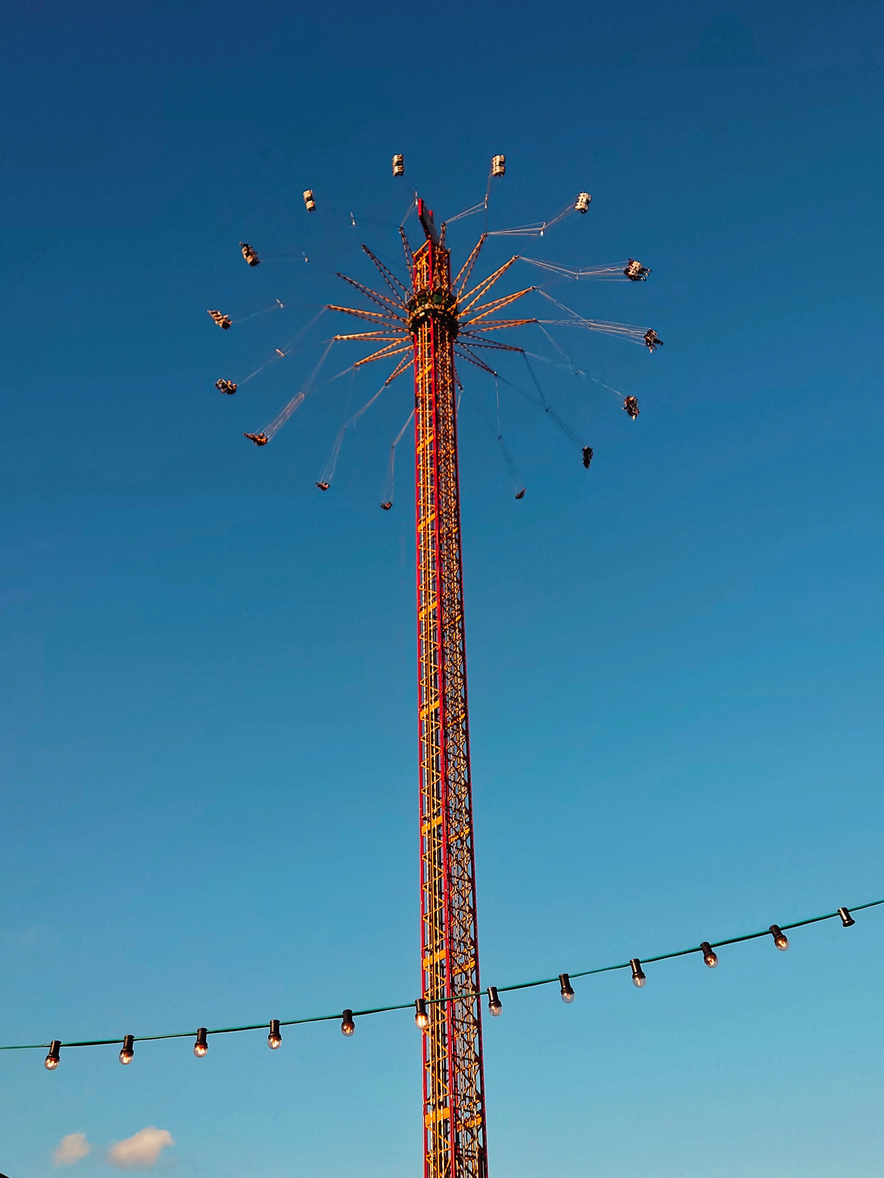 Photograph of a tall amusement ride with rotating chairs circling a lattice tower against a clear blue sky.