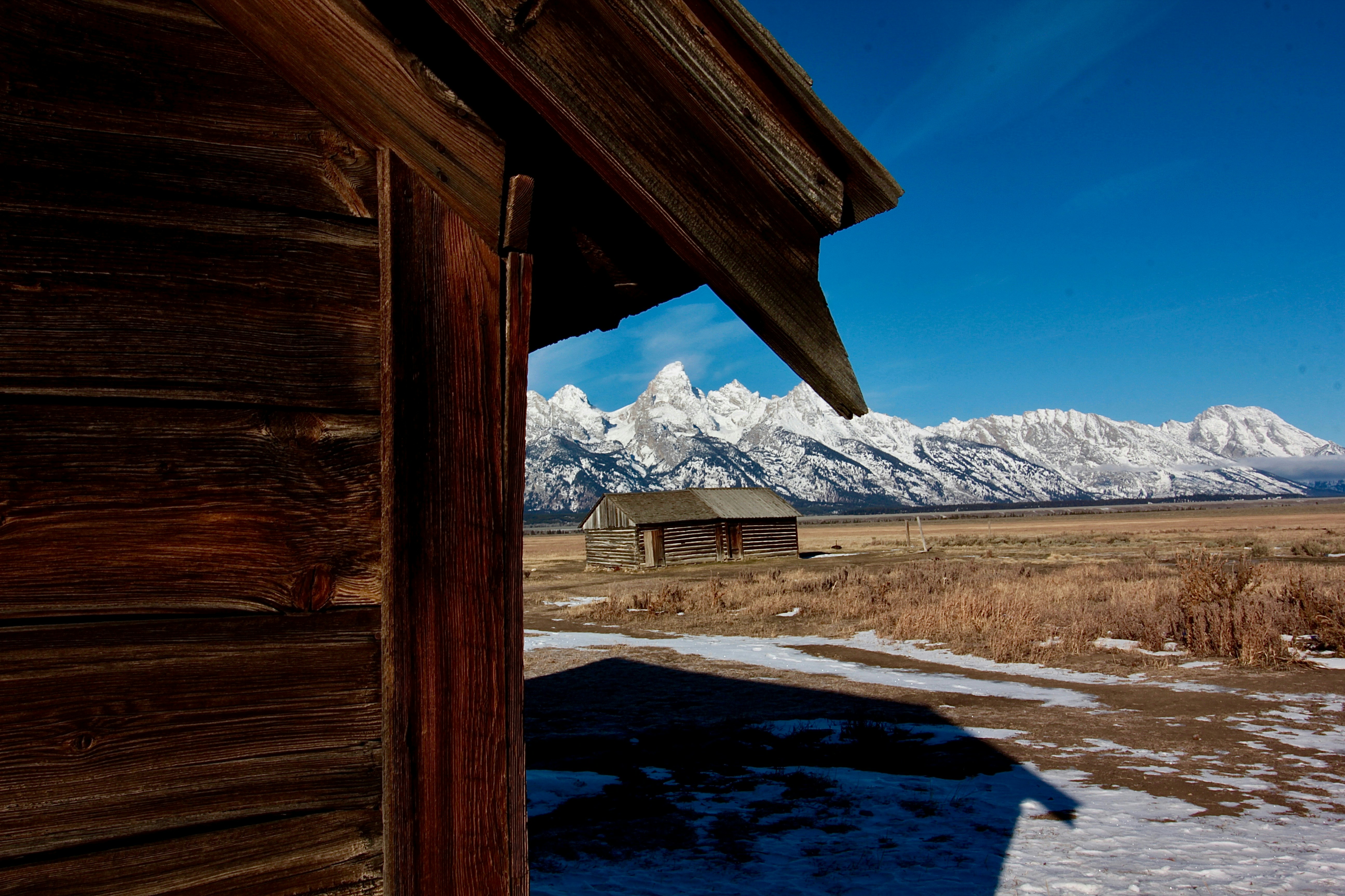 The Grand Teton range from Mormon Row in Grand Teton National Park | A house in the middle of a field with mountains in the background