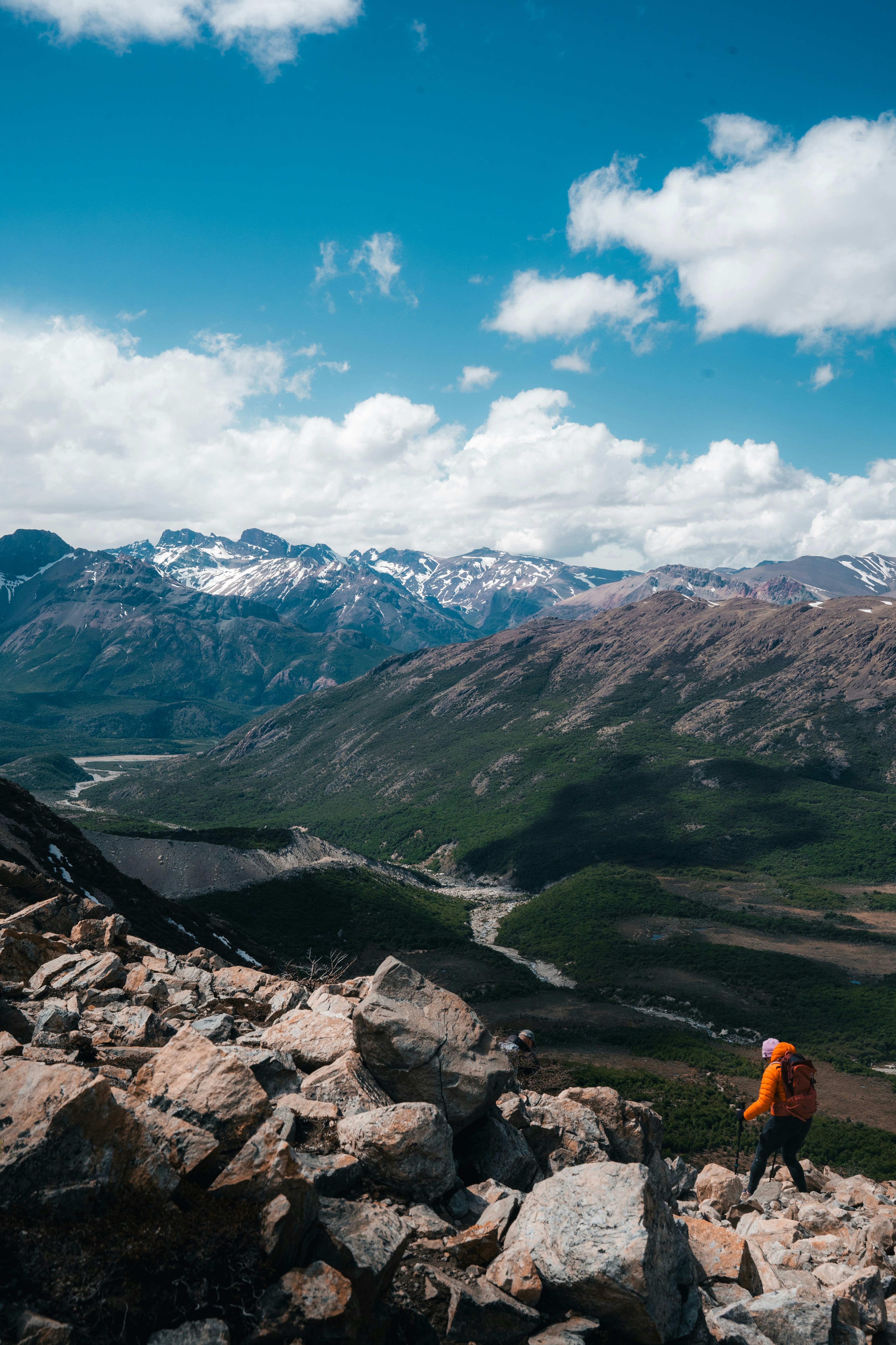 Orange-clad climber on sunlit scree beneath snow-dusted peaks