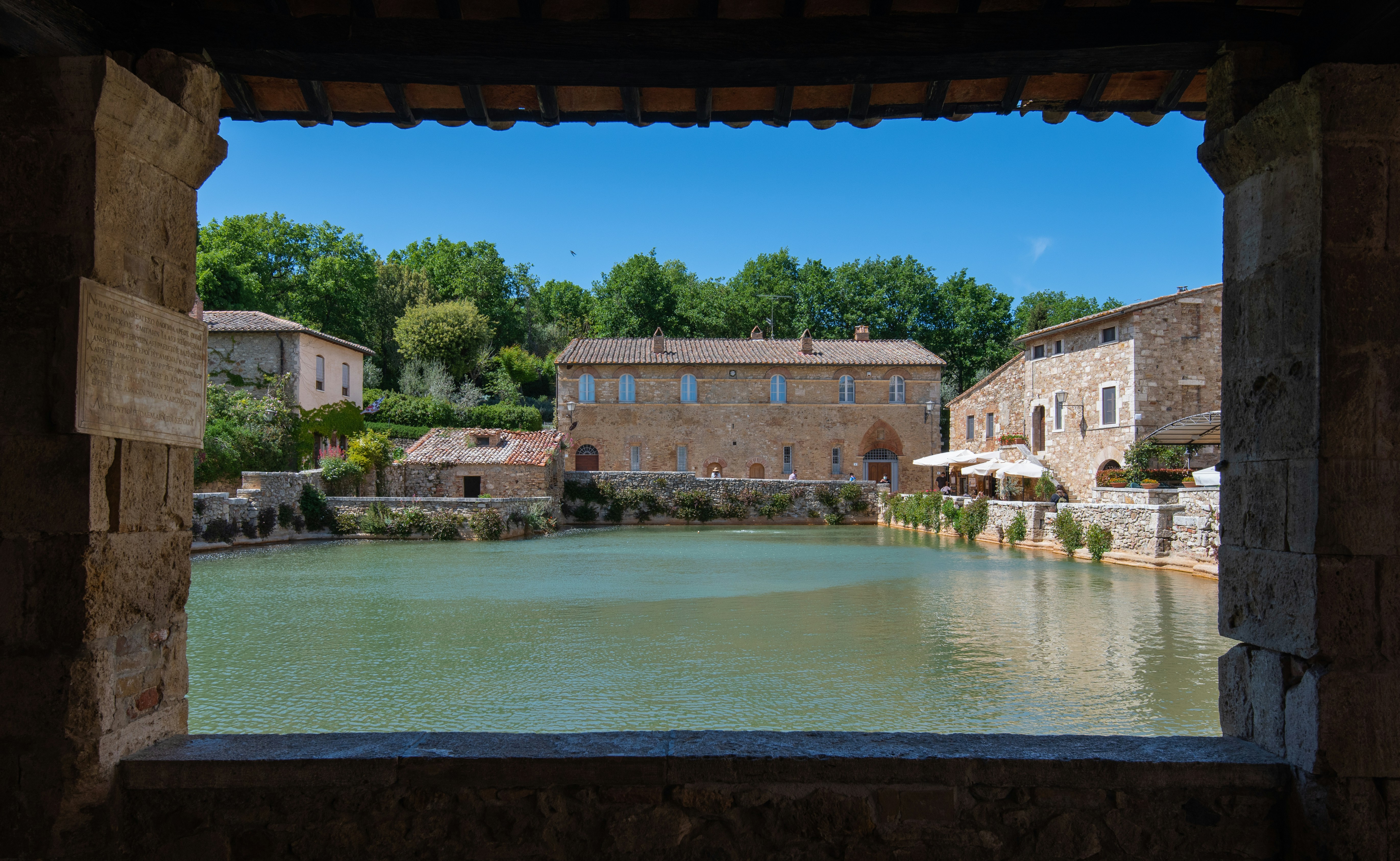 Scenic village buildings and a tranquil pond viewed through a stone-framed window.