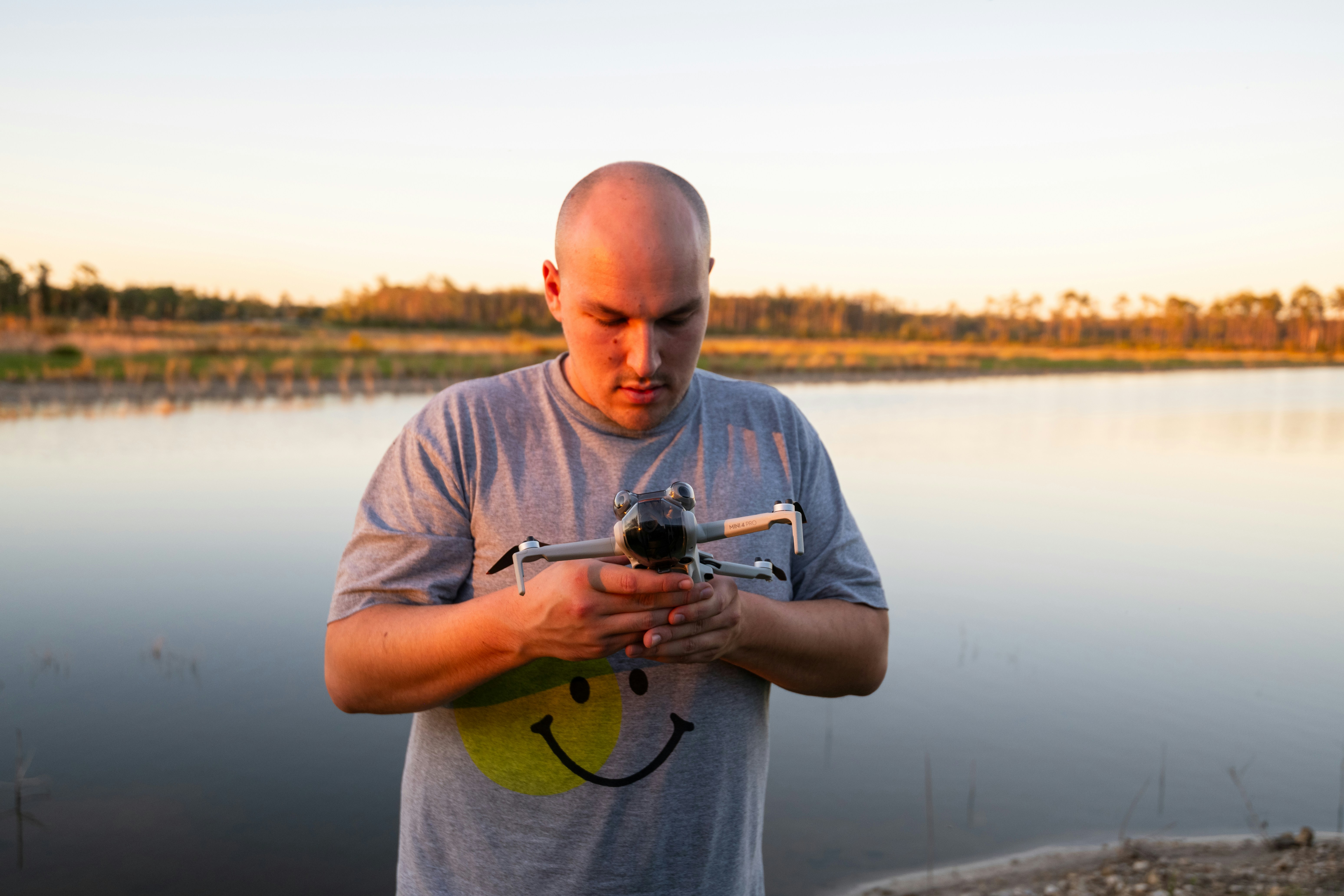 Person holding a DJI Mini 4 Pro drone near a serene lakeside during golden hour.