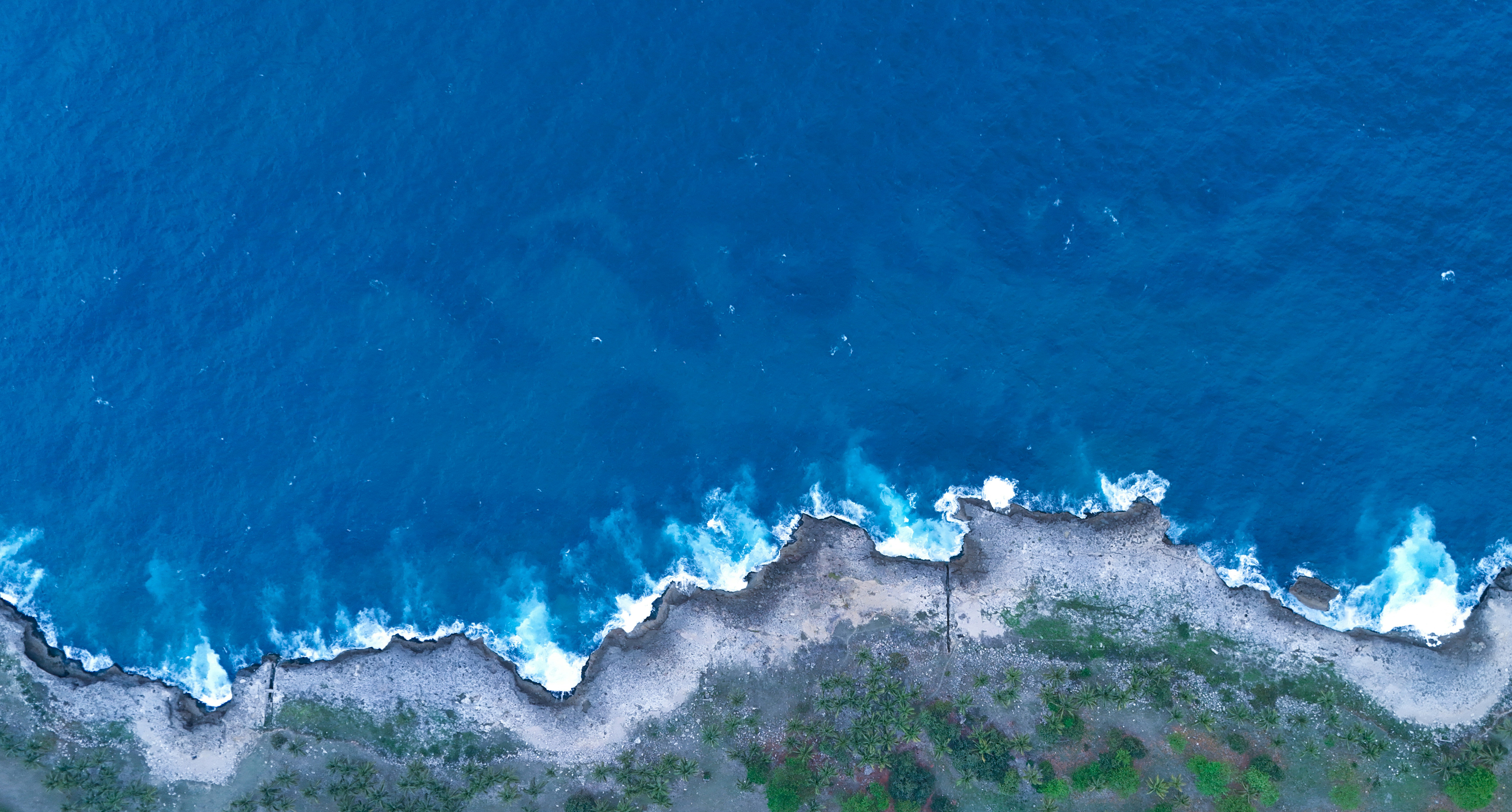 Aerial view of ocean waves meeting rugged coastline, creating a contrasting boundary between deep blue water and rocky shore.