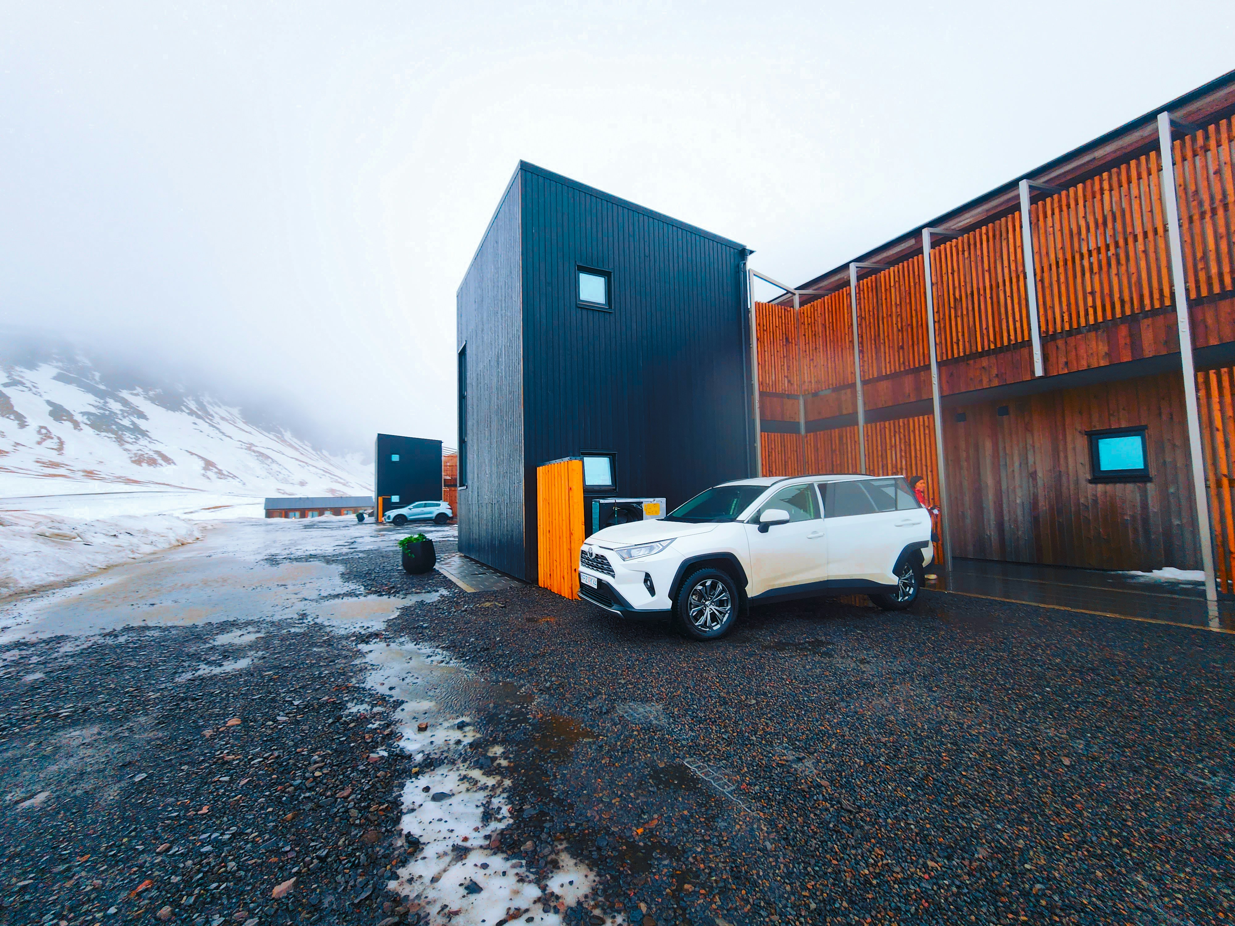 White SUV by a timber-clad lodge under a pale alpine sky