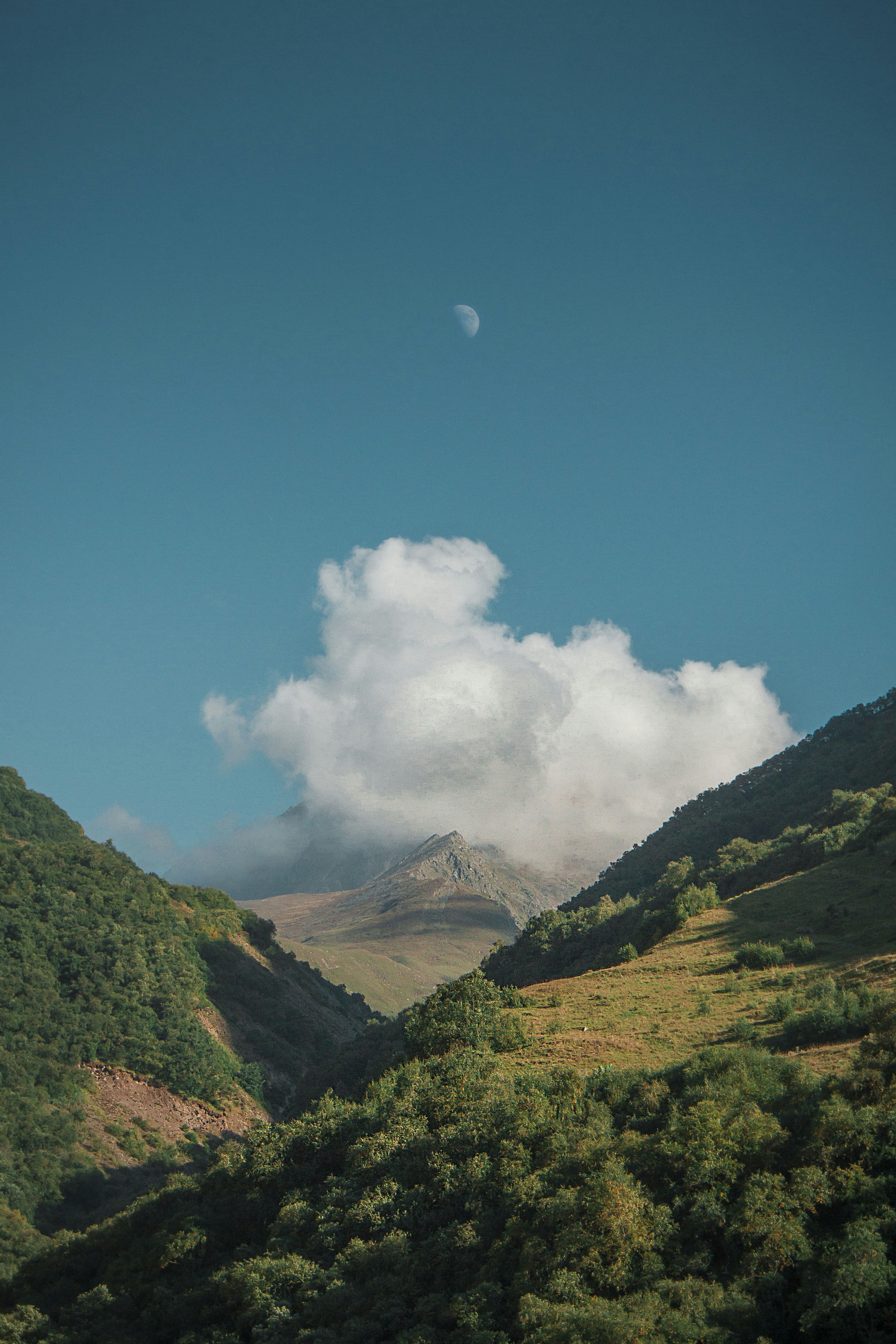 Crescent Moon Over the Verdant Ridge: Clouds Crown a Mountain Sentinel