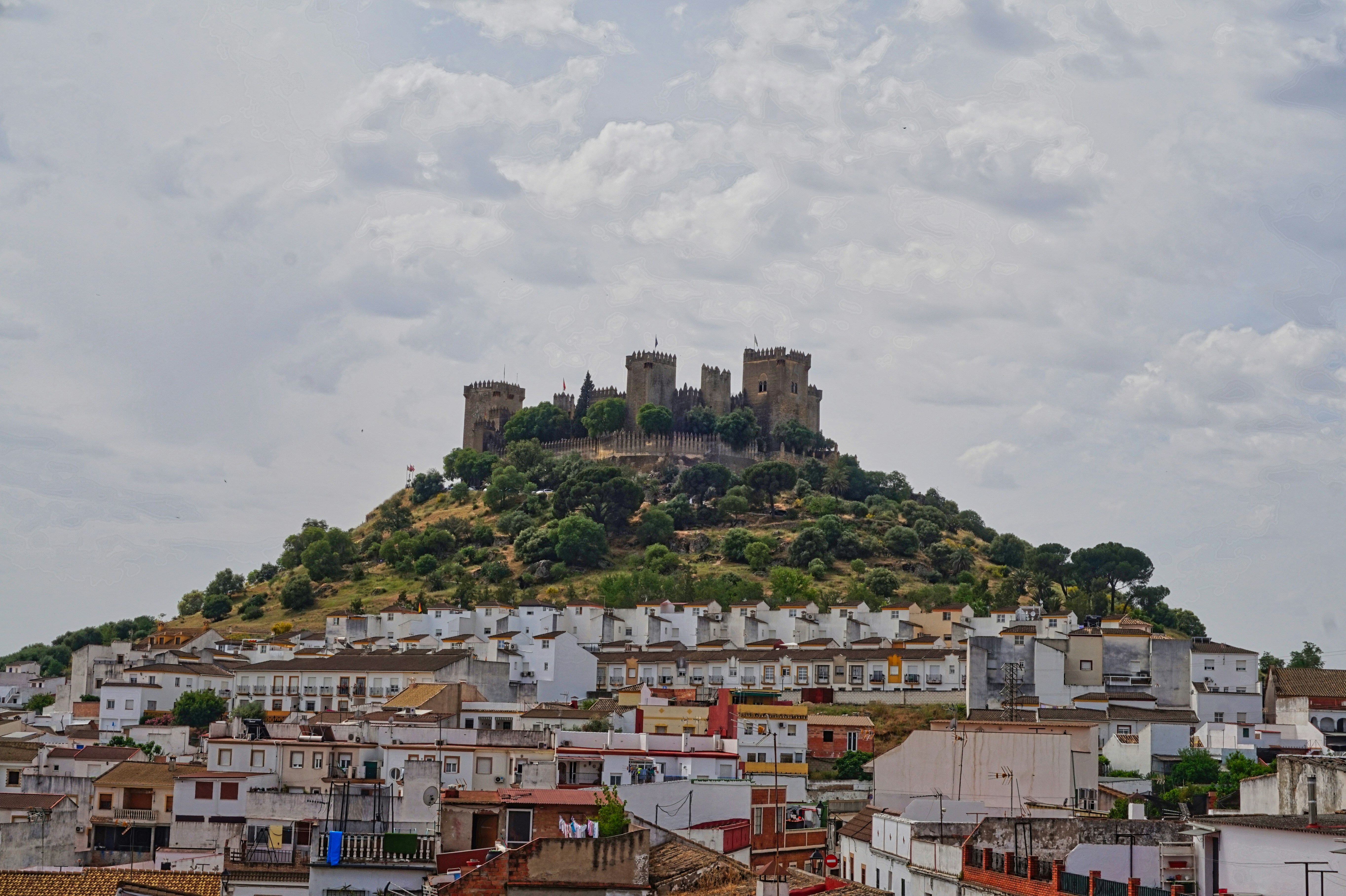 Castle perched atop a hill surrounded by a cluster of whitewashed village buildings under a cloudy sky.
