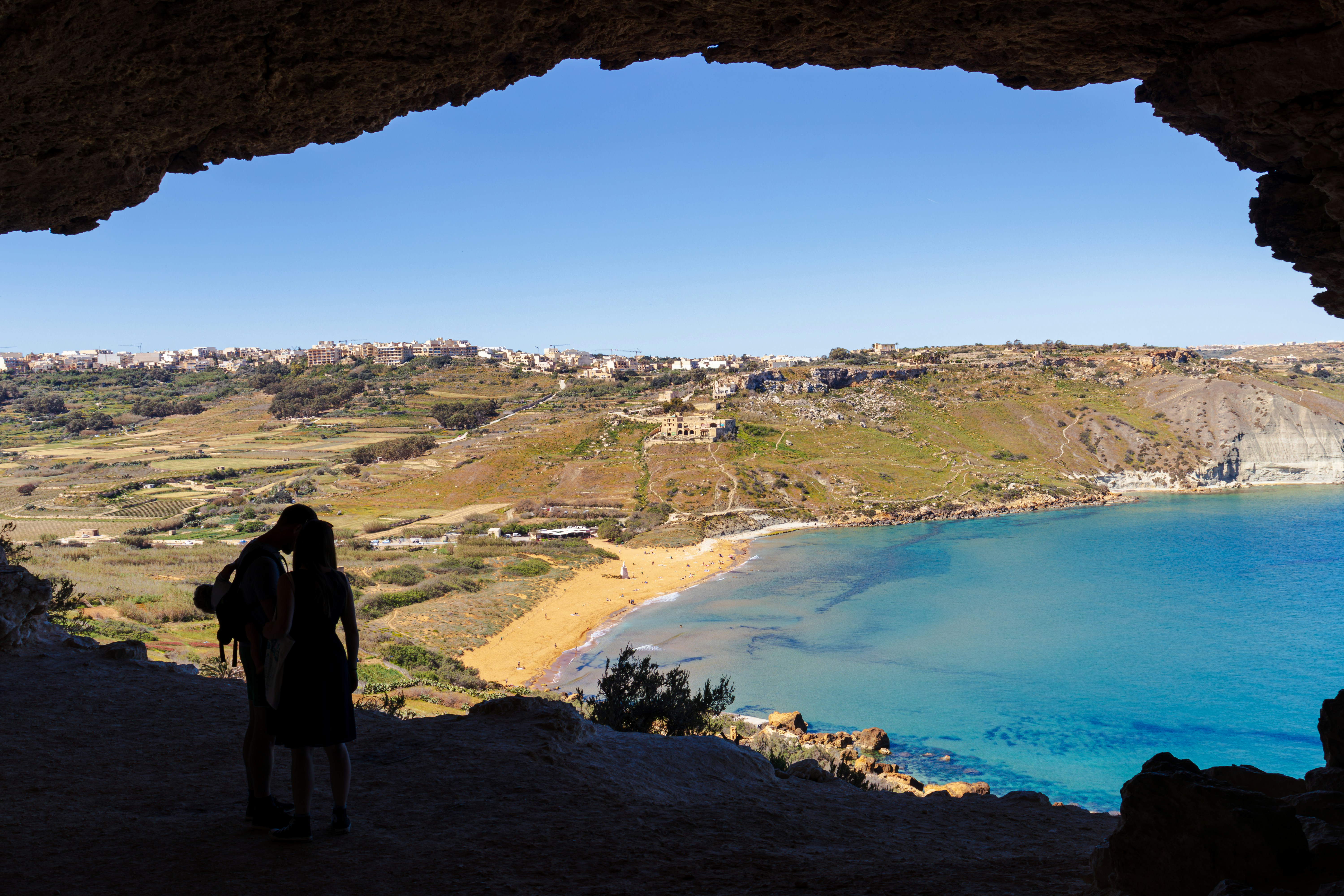Silhouette at the Cave Window: Two Explorers Over a Turquoise Bay