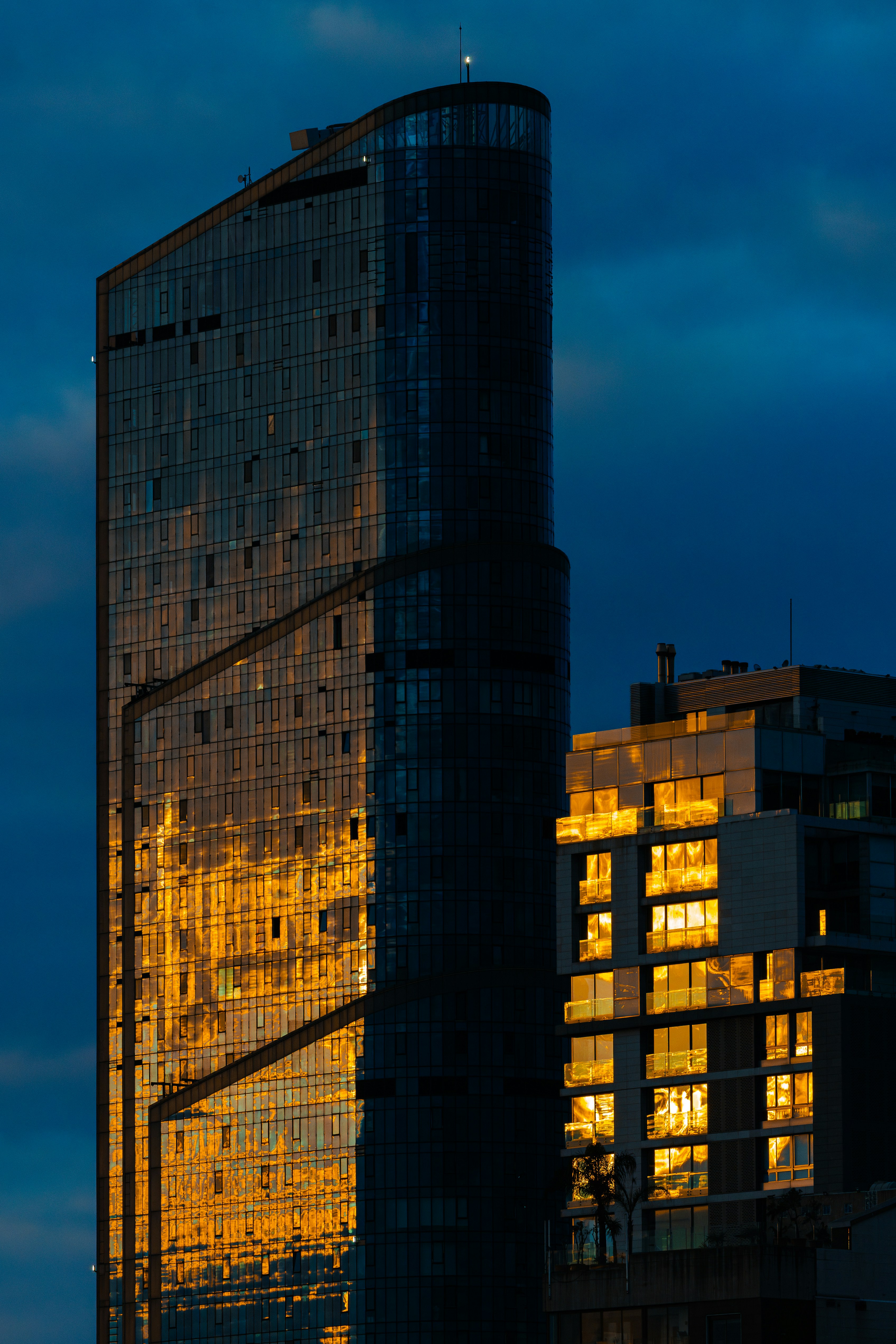 Golden Reflections on a Curved Glass Tower at Blue Hour