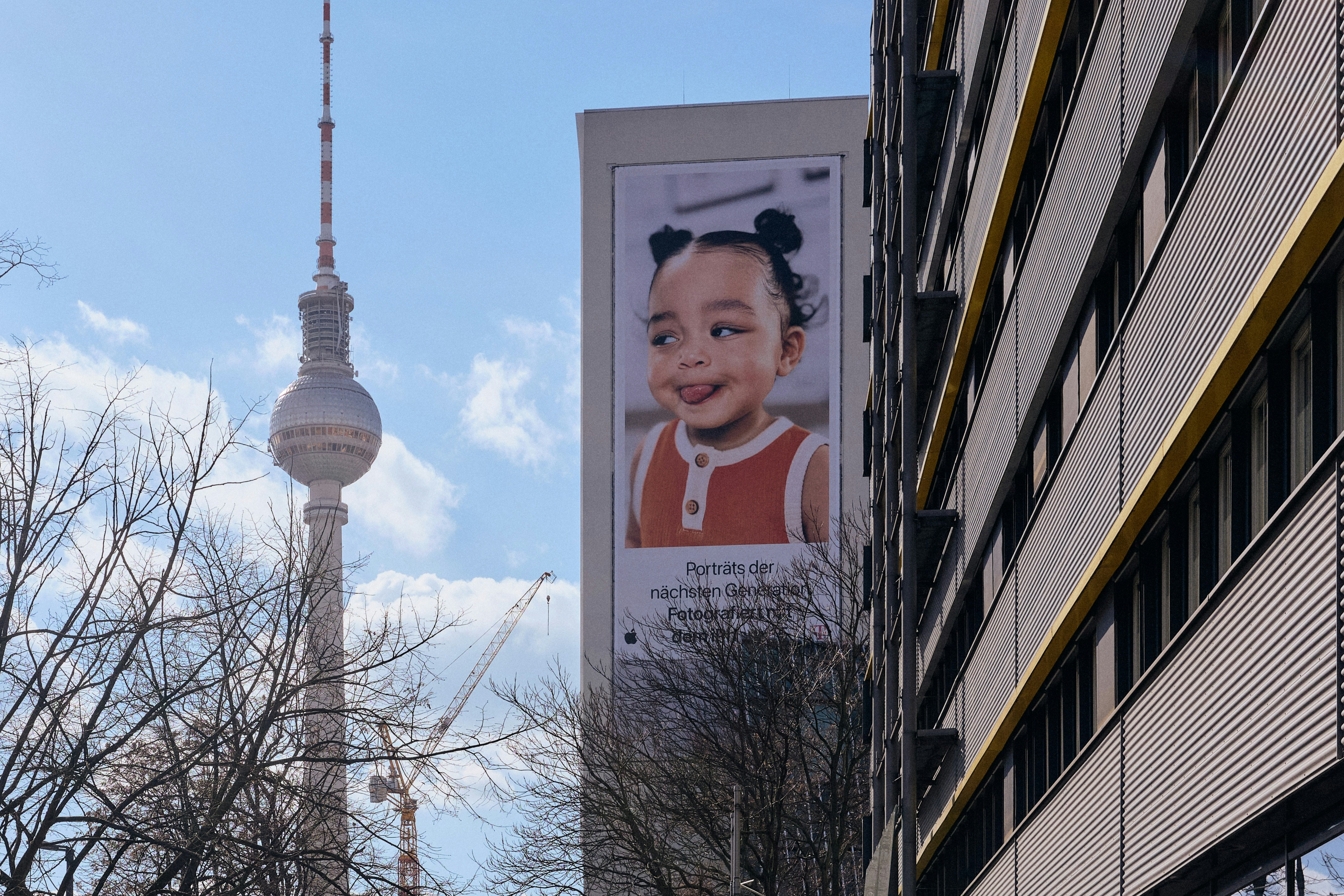Billboard featuring a smiling child on a city building facade next to a tall tower under a blue sky.
