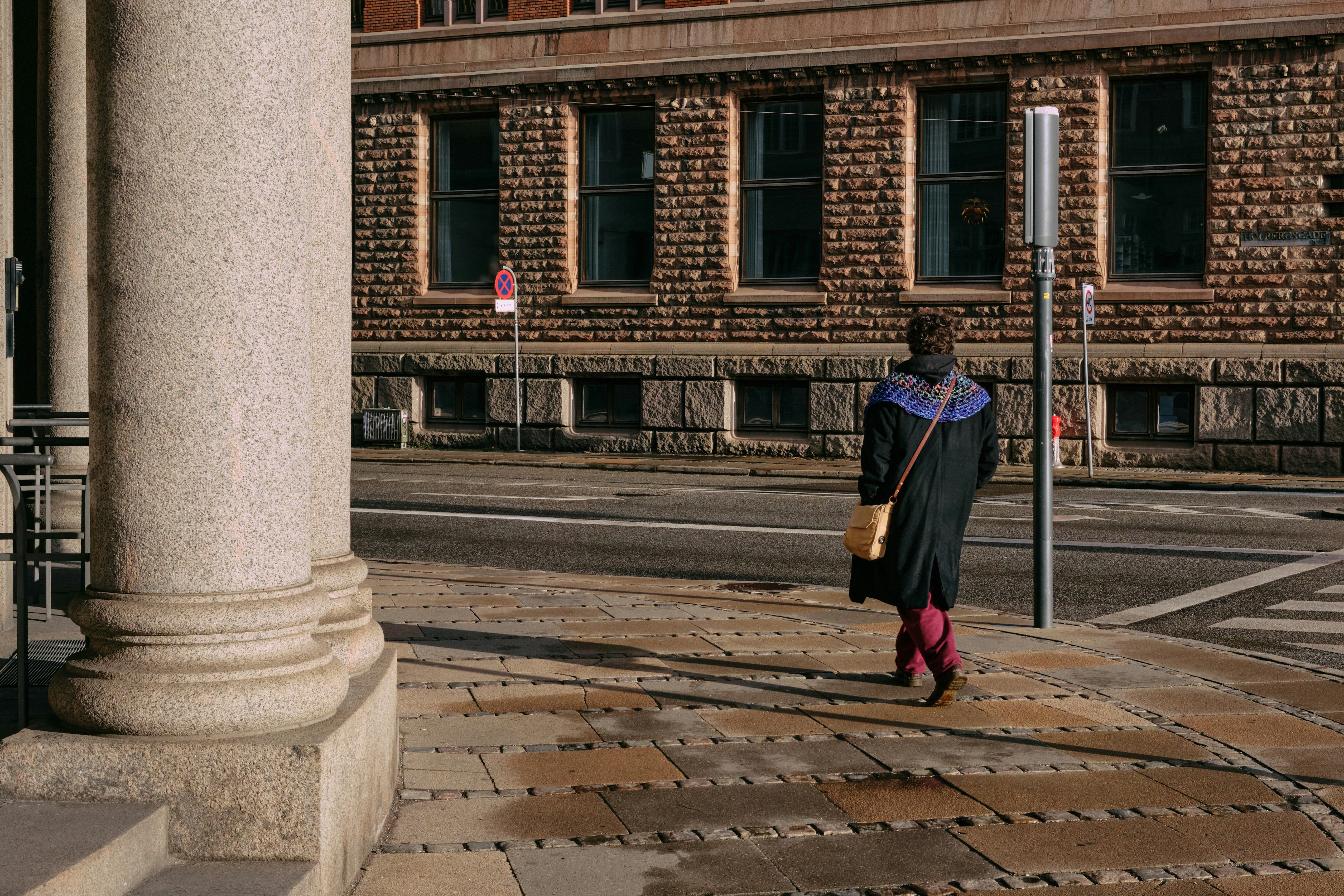 Clad in color, a lone walker crosses a sunlit urban plaza