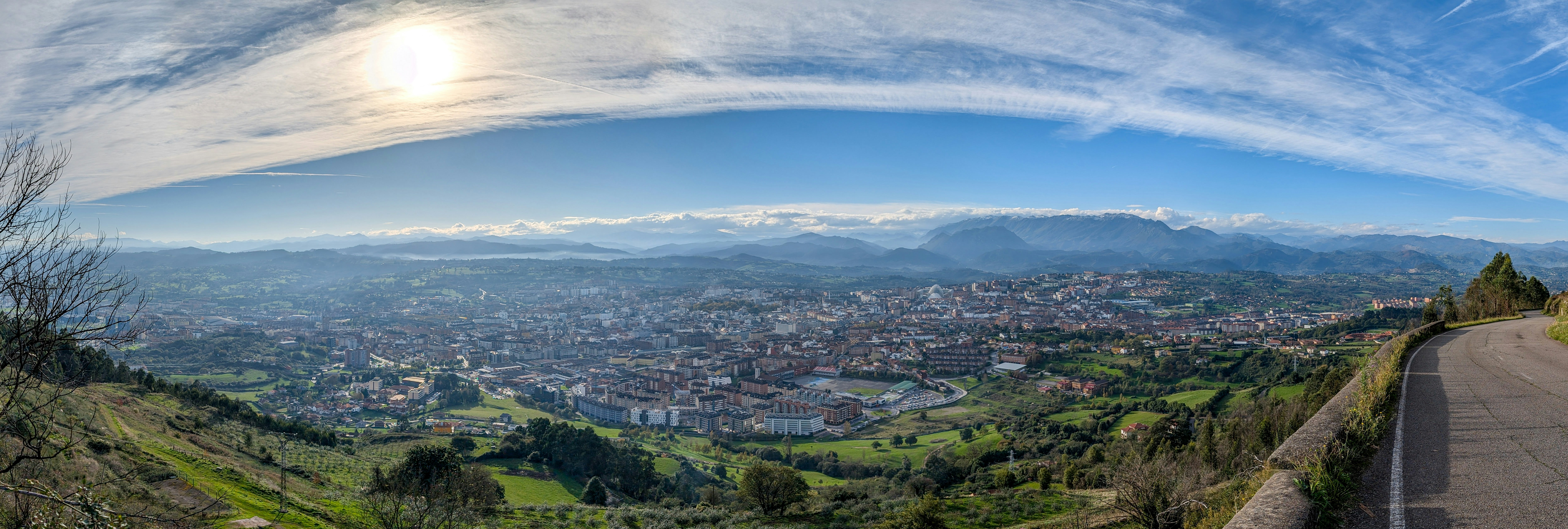 Expansive view of a cityscape nestled between verdant hills under a sunlit sky.