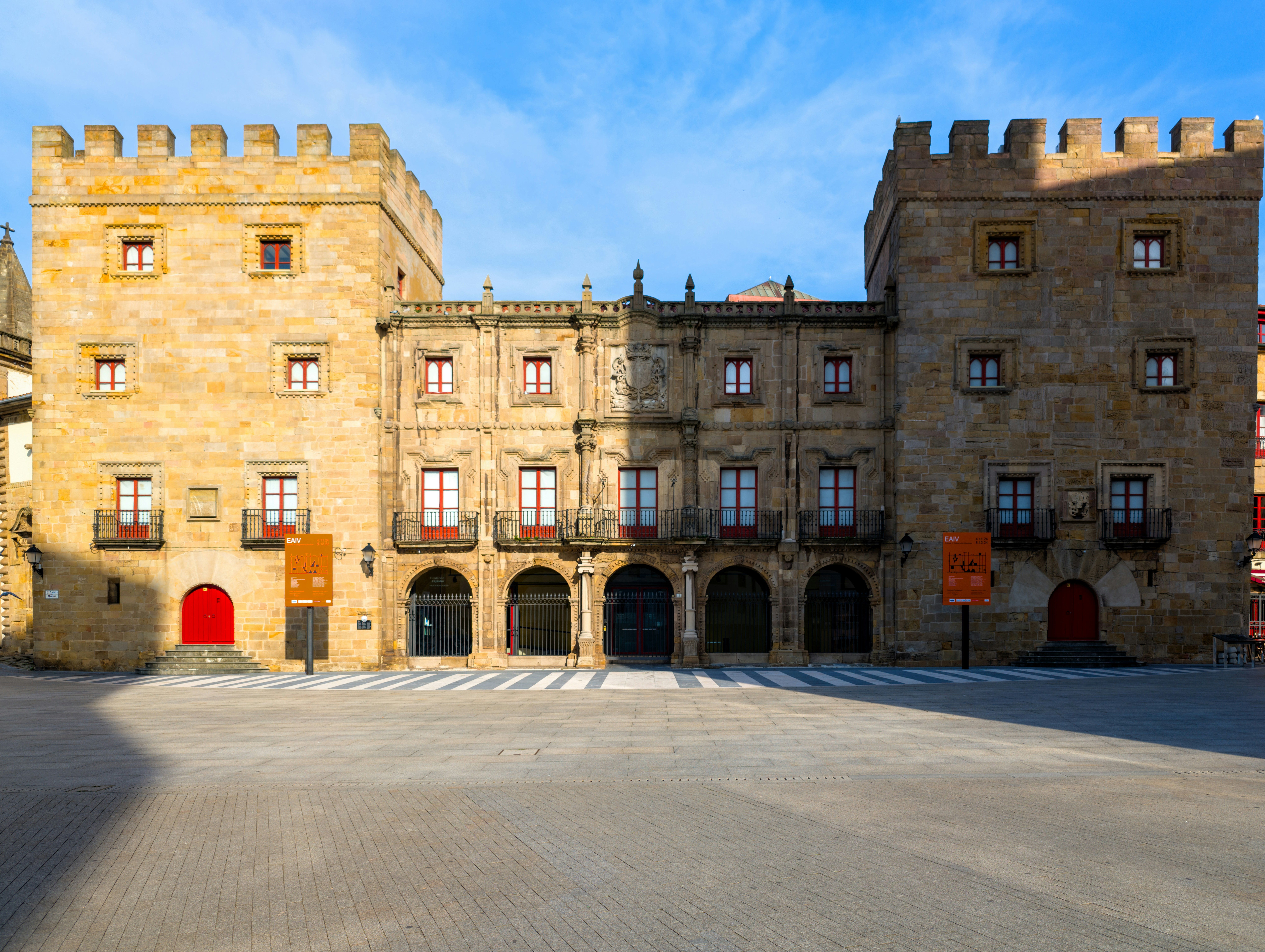 Large stone building with a striking red door and crenelated towers under a clear blue sky.
