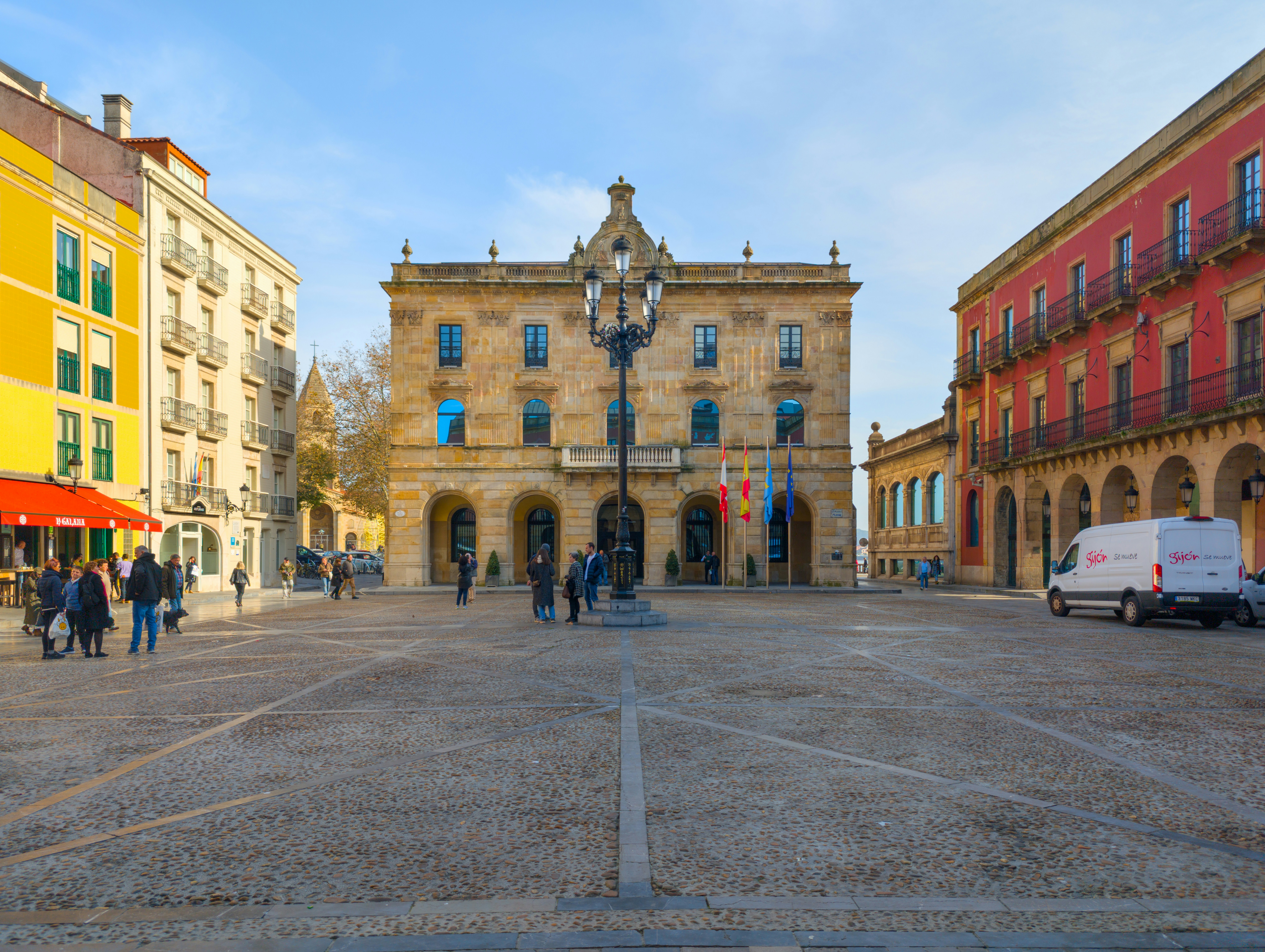 Sunny plaza framed by vibrant buildings and a central clock tower.