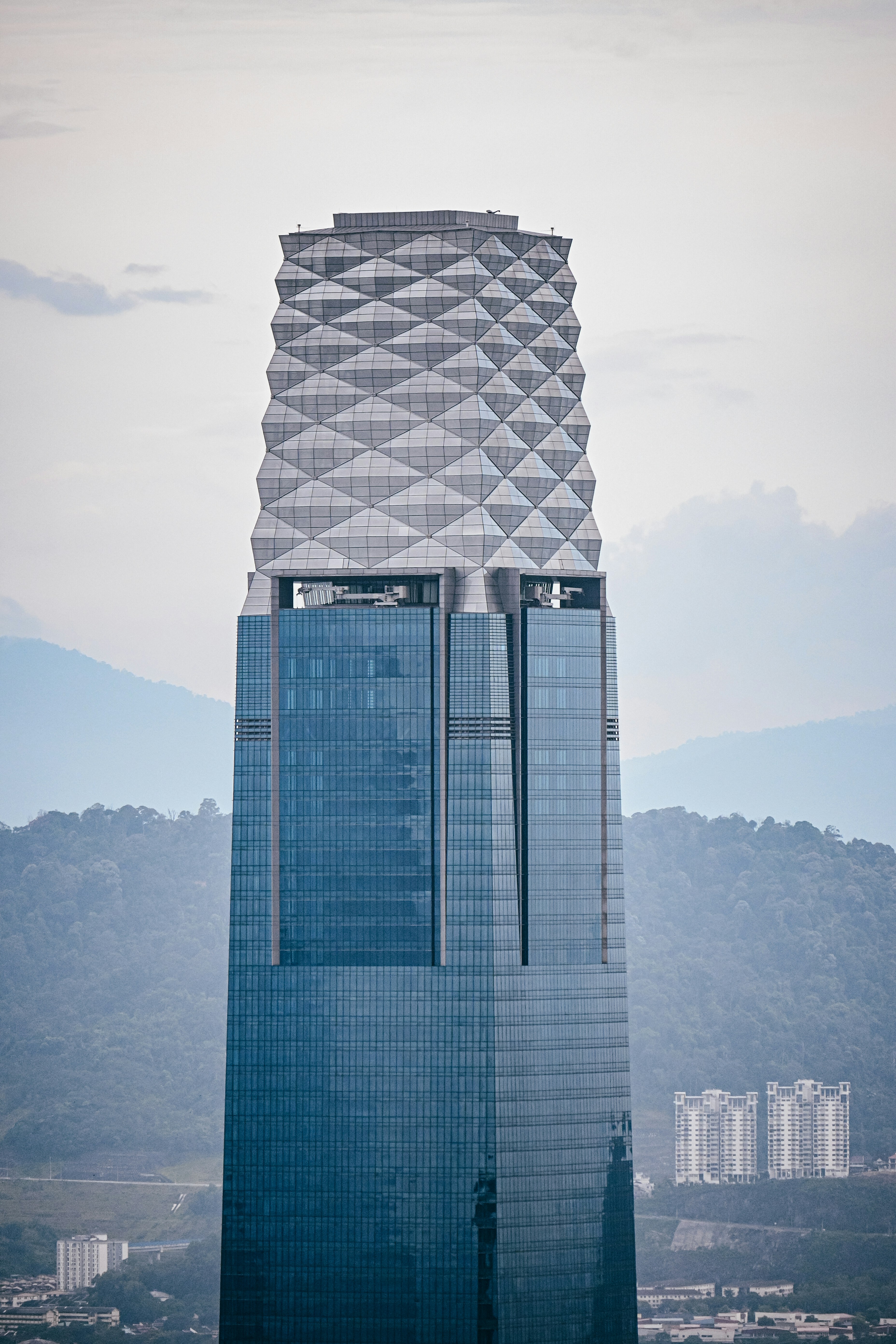 Photograph of a glass-clad skyscraper with a diamond-patterned crown rising above a hazy valley.