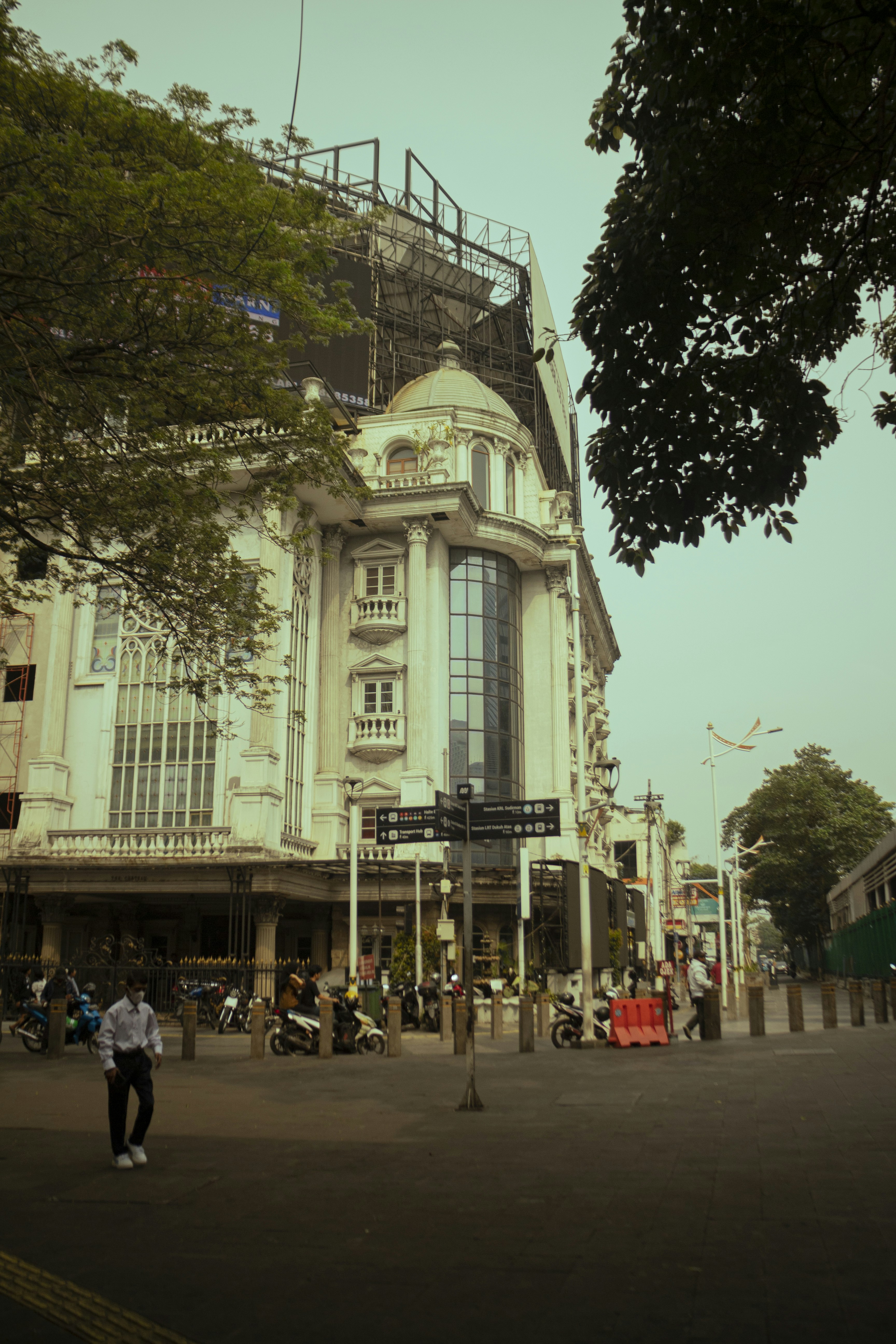 Historic building with intricate architectural details and modern signage in a bustling urban setting. A lone figure walks along the street, adding a sense of scale.