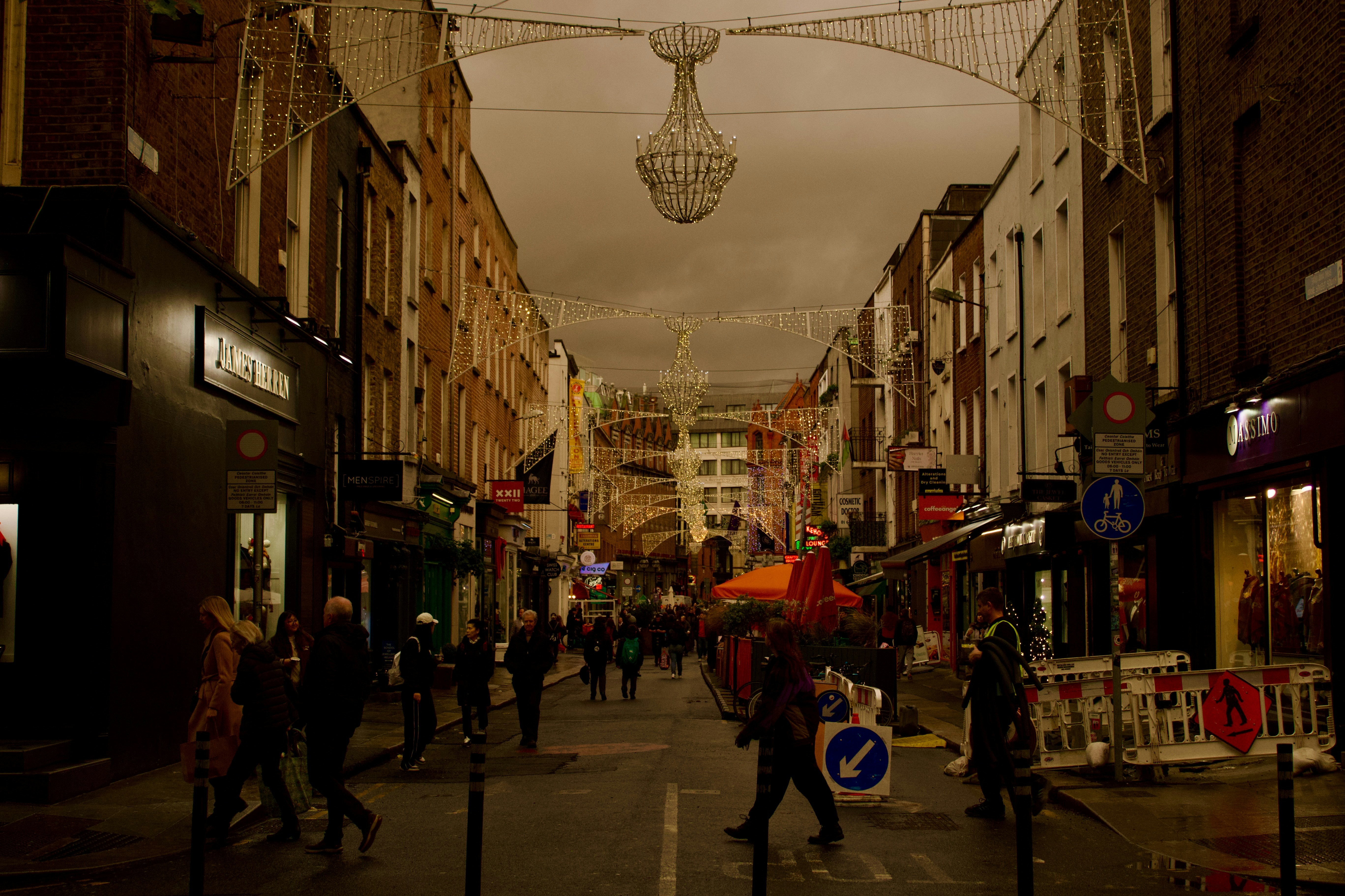 Busy pedestrian street in Dublin lined with shops under a cloudy evening sky.