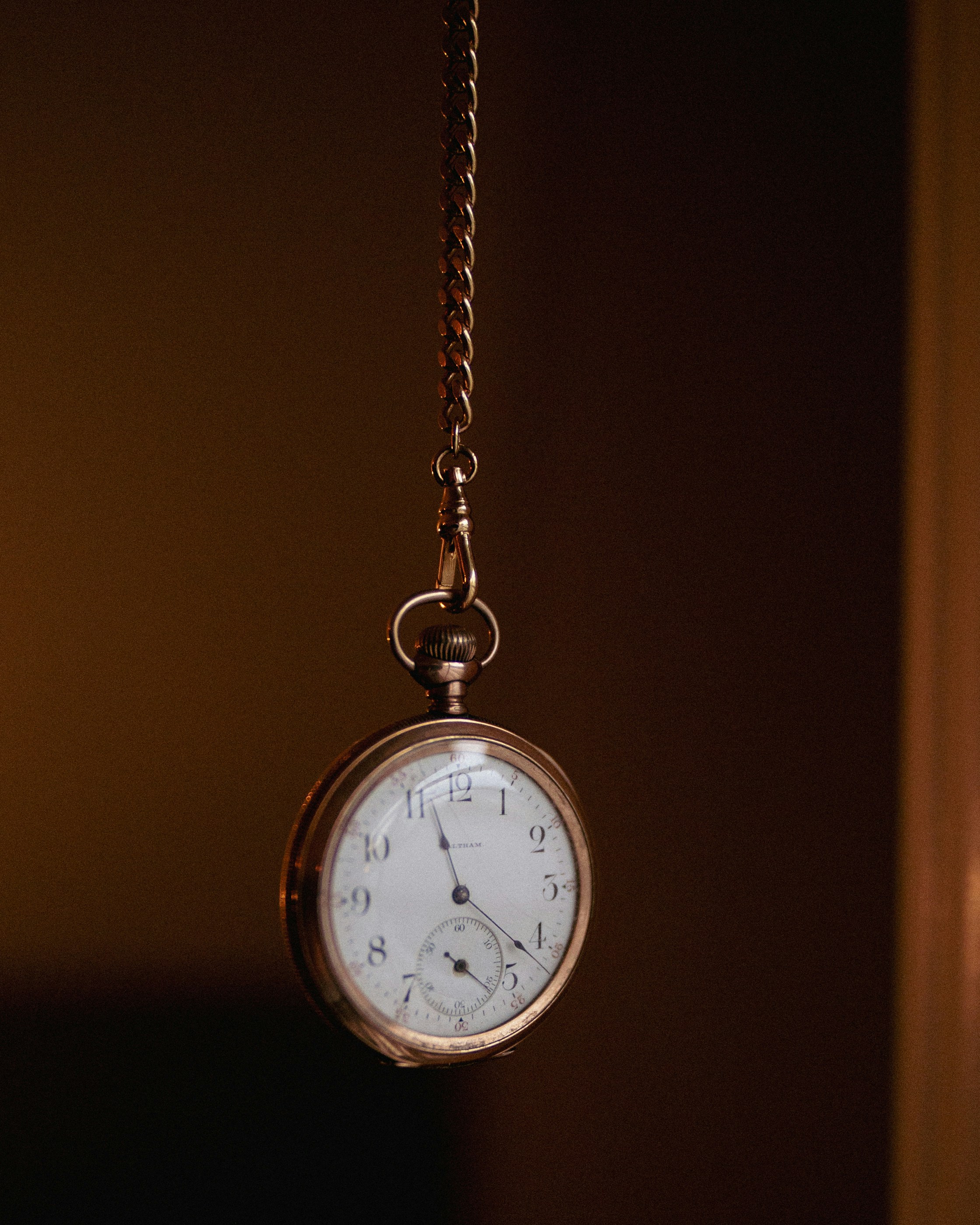 A pocket watch hanging from a chain in a dark room photo – Free Clock ...