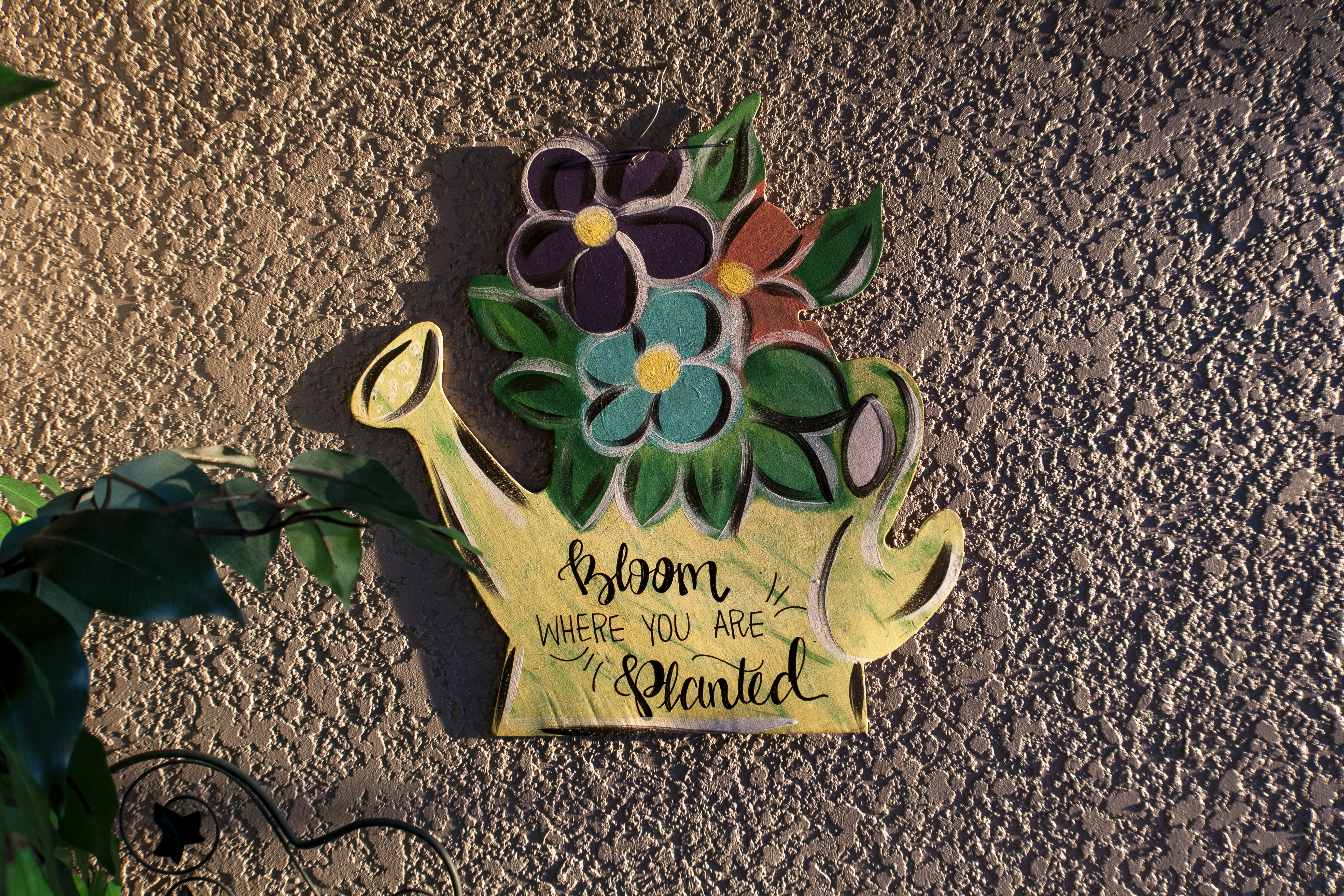 Colorful watering can decoration adorned with flowers and an inspirational message about growth on a textured wall.