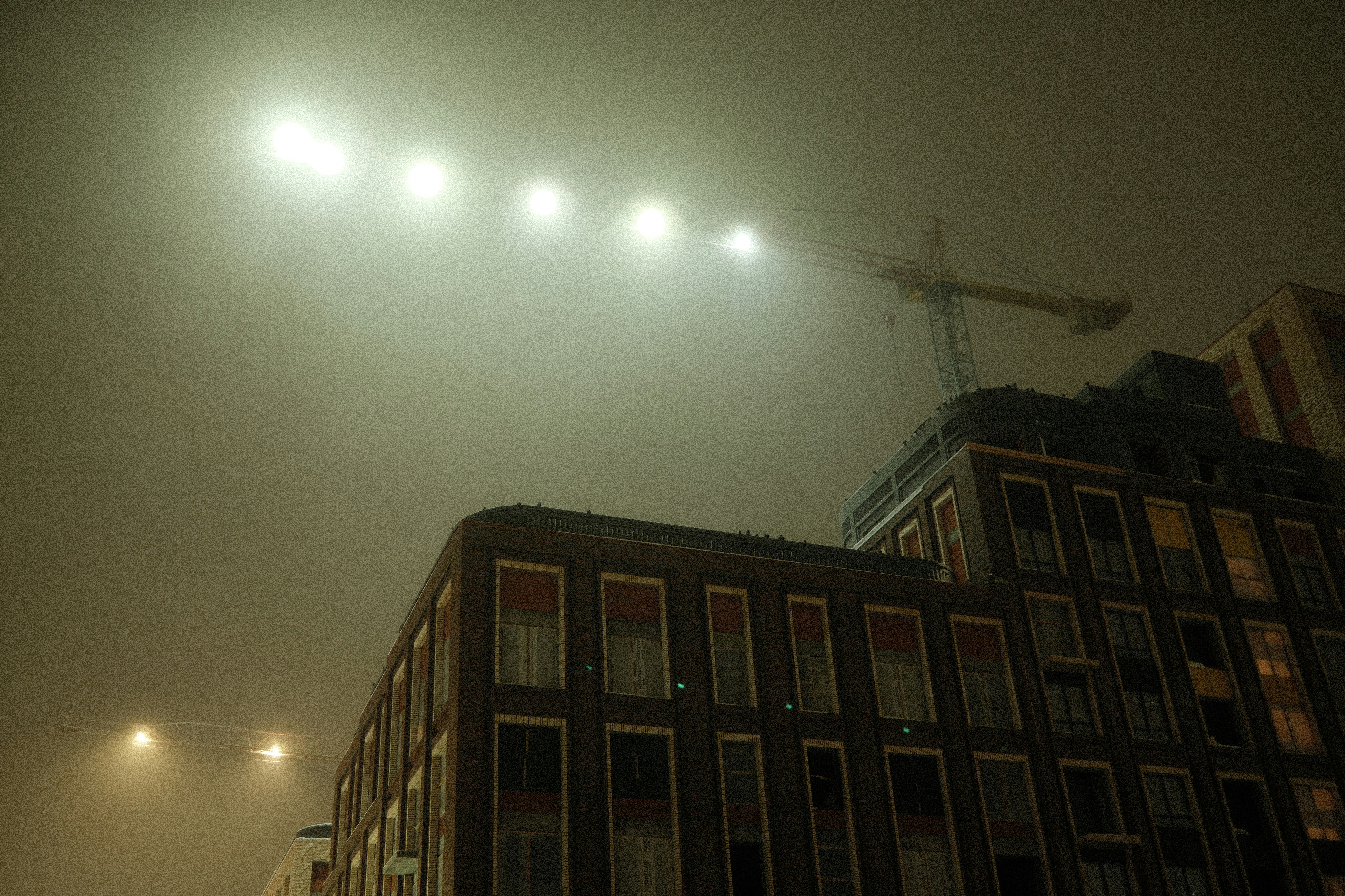 Crane Lights Cut Through Fog Over Stoic Brickwork