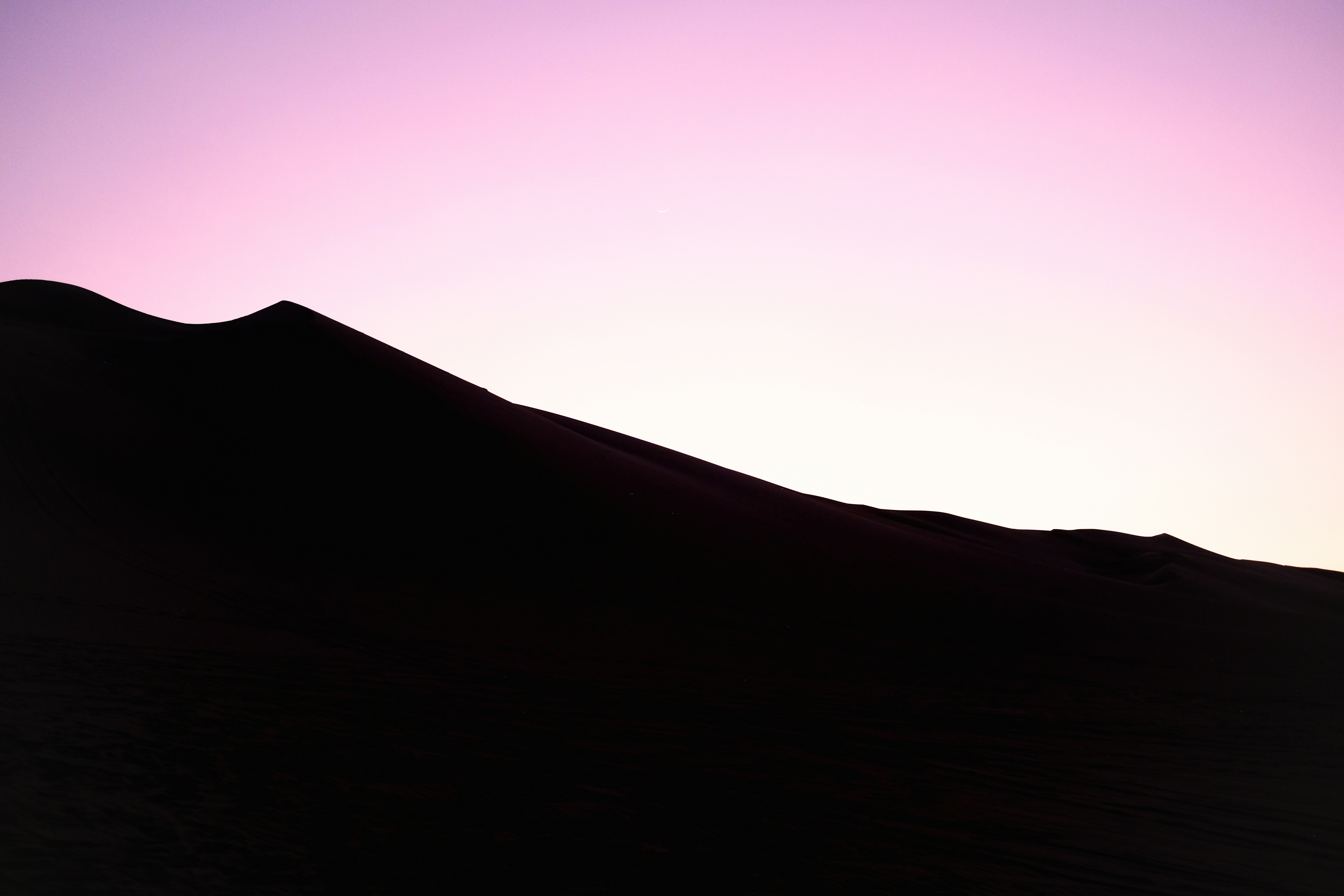 Silhouette of a sand dune against a soft pink and purple sky at sunset.