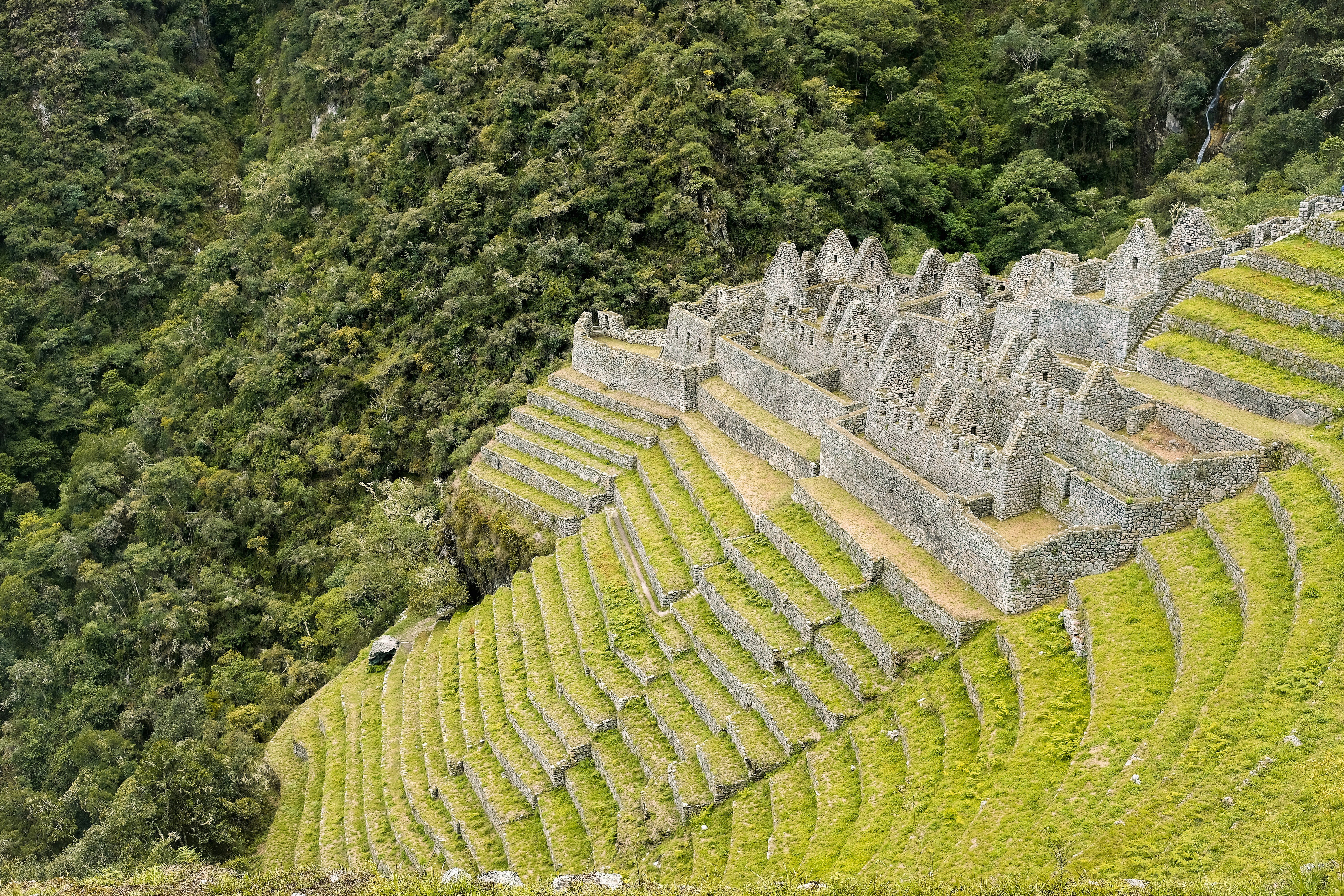 Ancient stone ruins nestled within lush, green terraced hills under soft, diffused lighting.