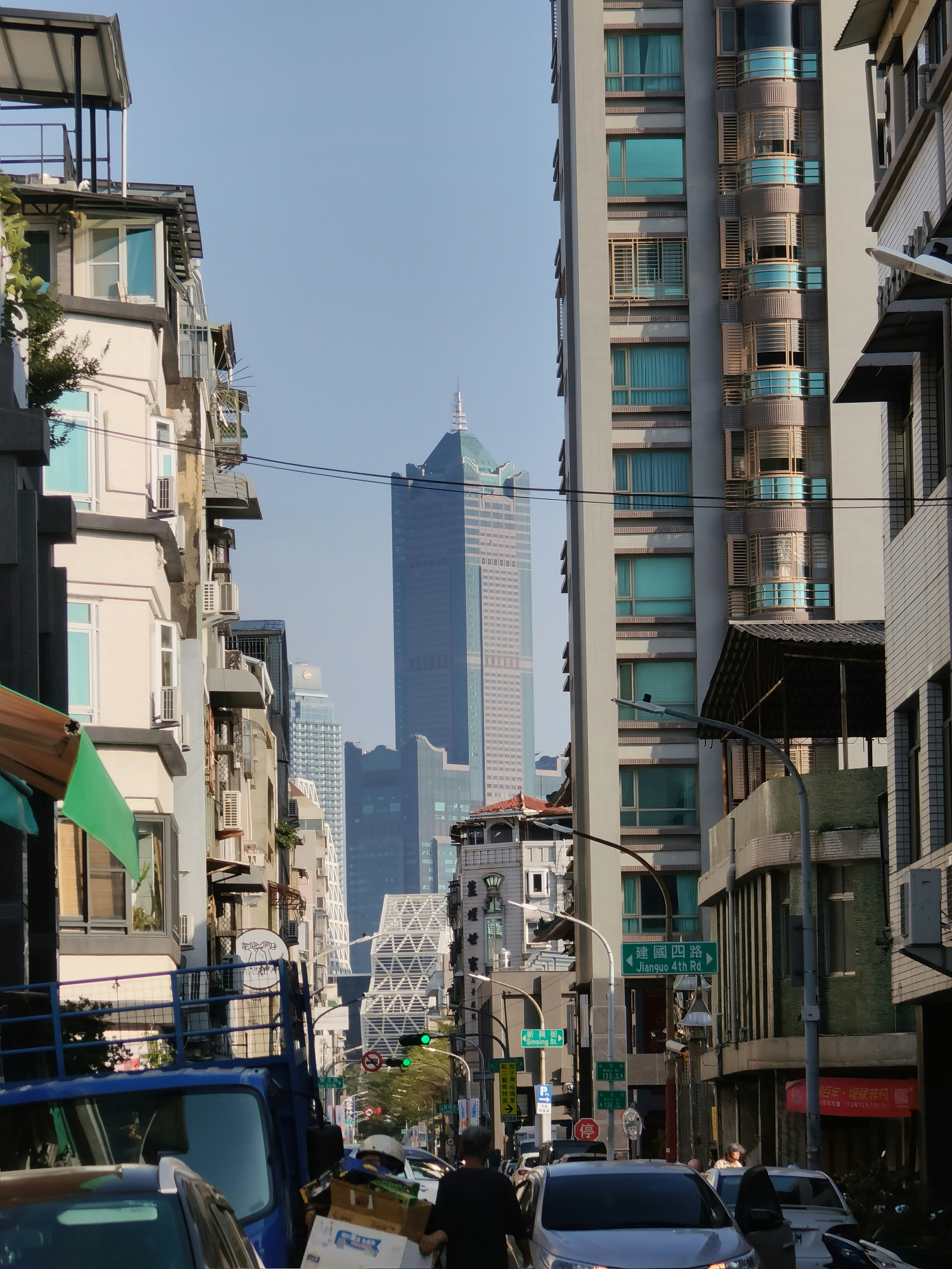 Urban street scene with mid-rise buildings funneling toward a distant blue glass tower.