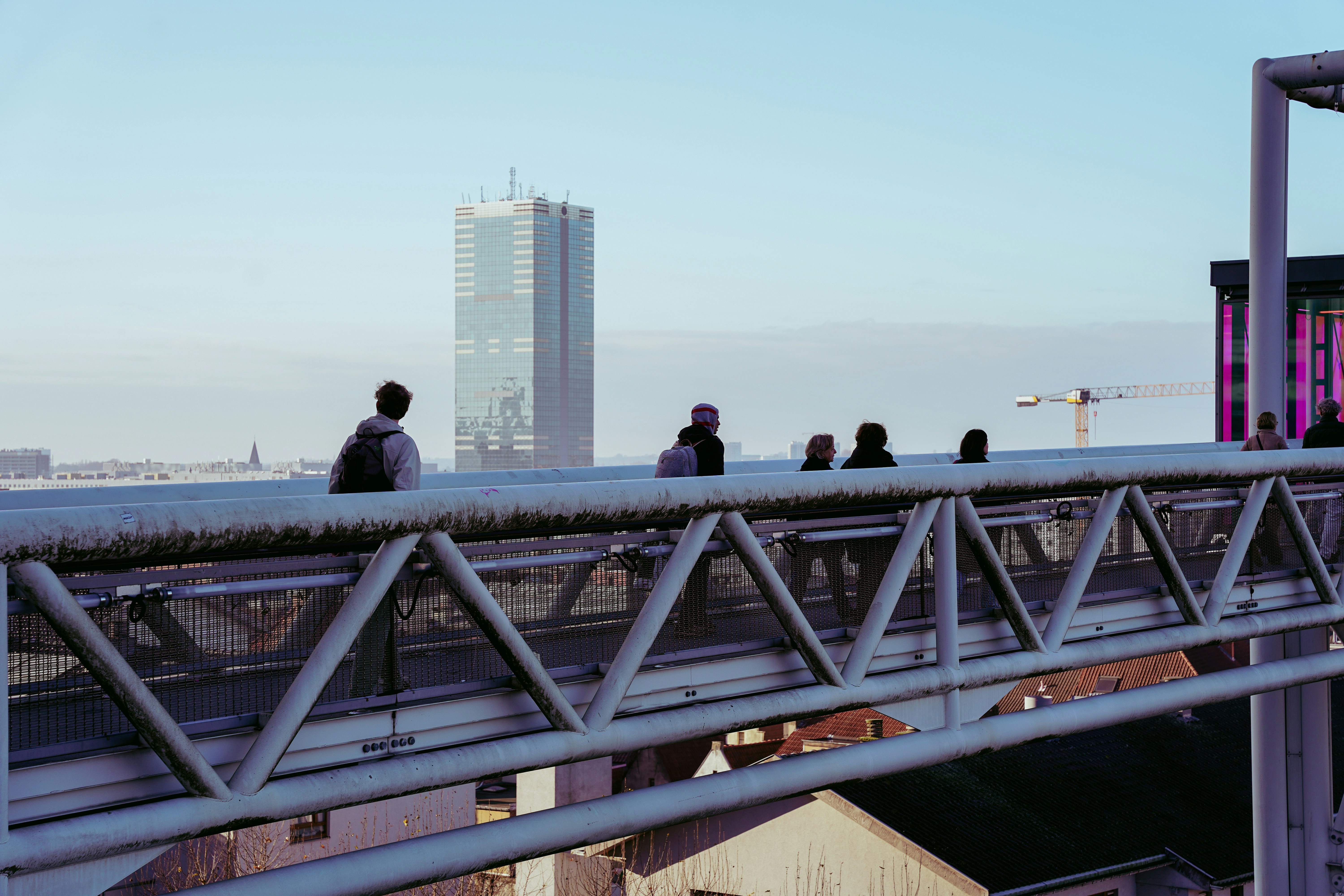 People walking on a modern elevated walkway with a cityscape backdrop at dusk.