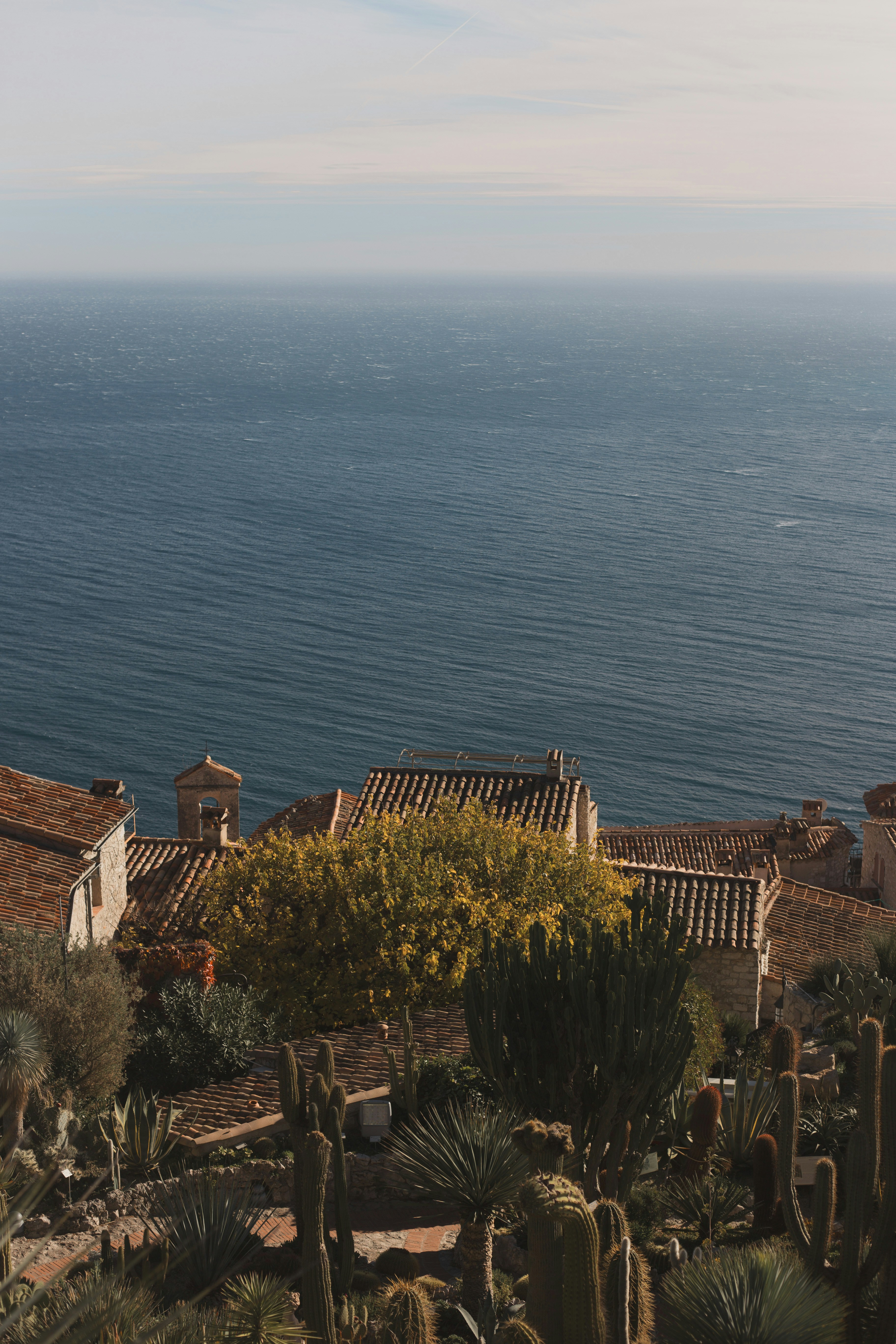 Terracotta rooftops and lush greenery blend with the expansive blue sea under a soft sky.