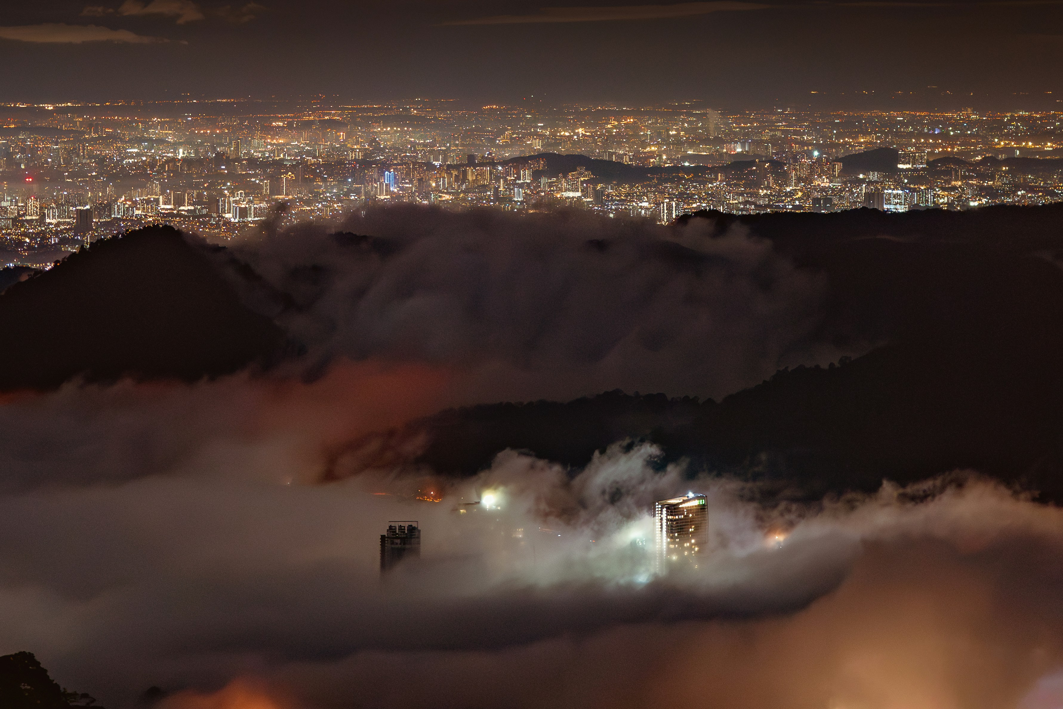 City lights of Kuala Lumpur illuminate the night sky from above the misty Genting mountains.