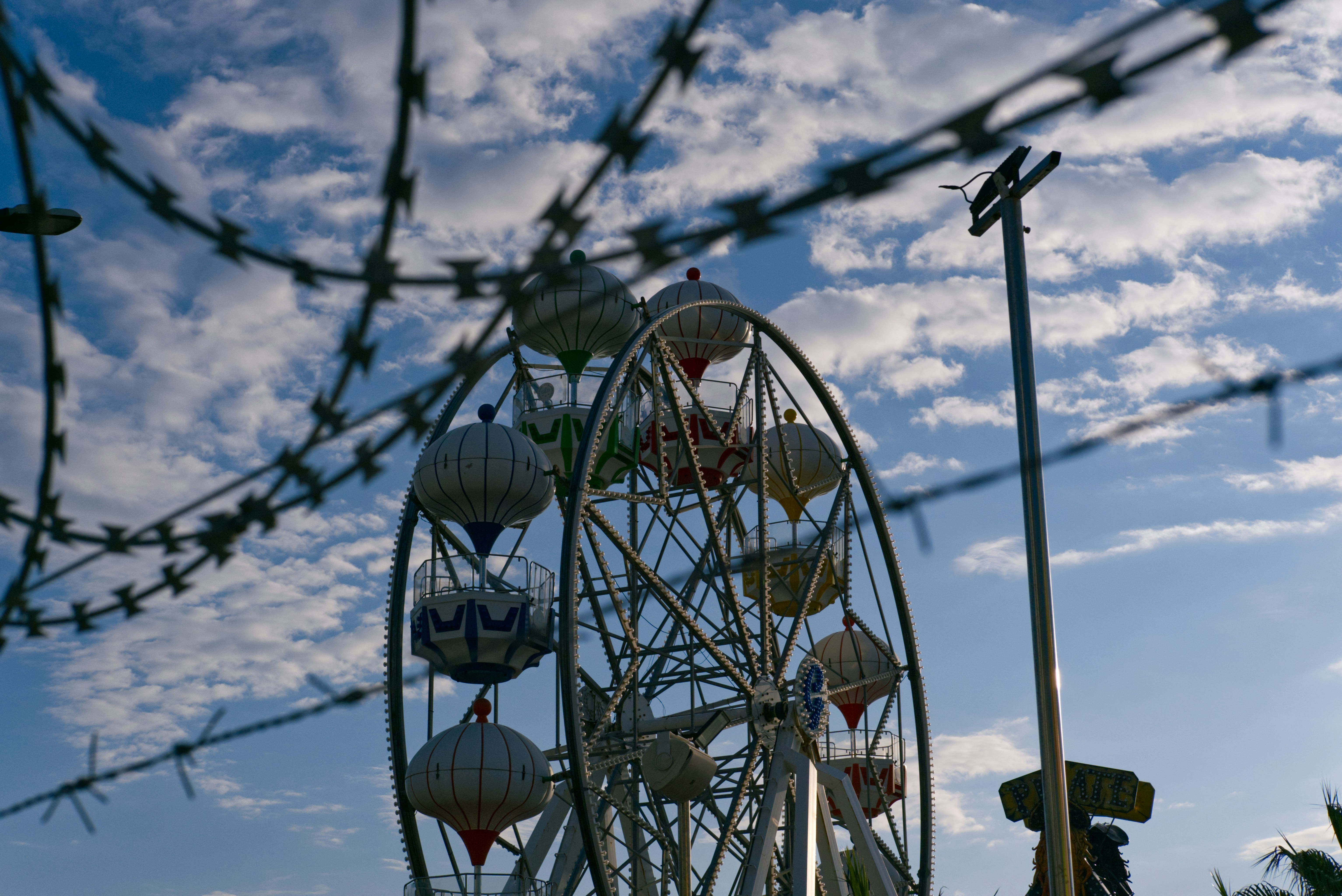 Barbed-Wire Frame: Ferris Wheel Against a Clear Blue Sky