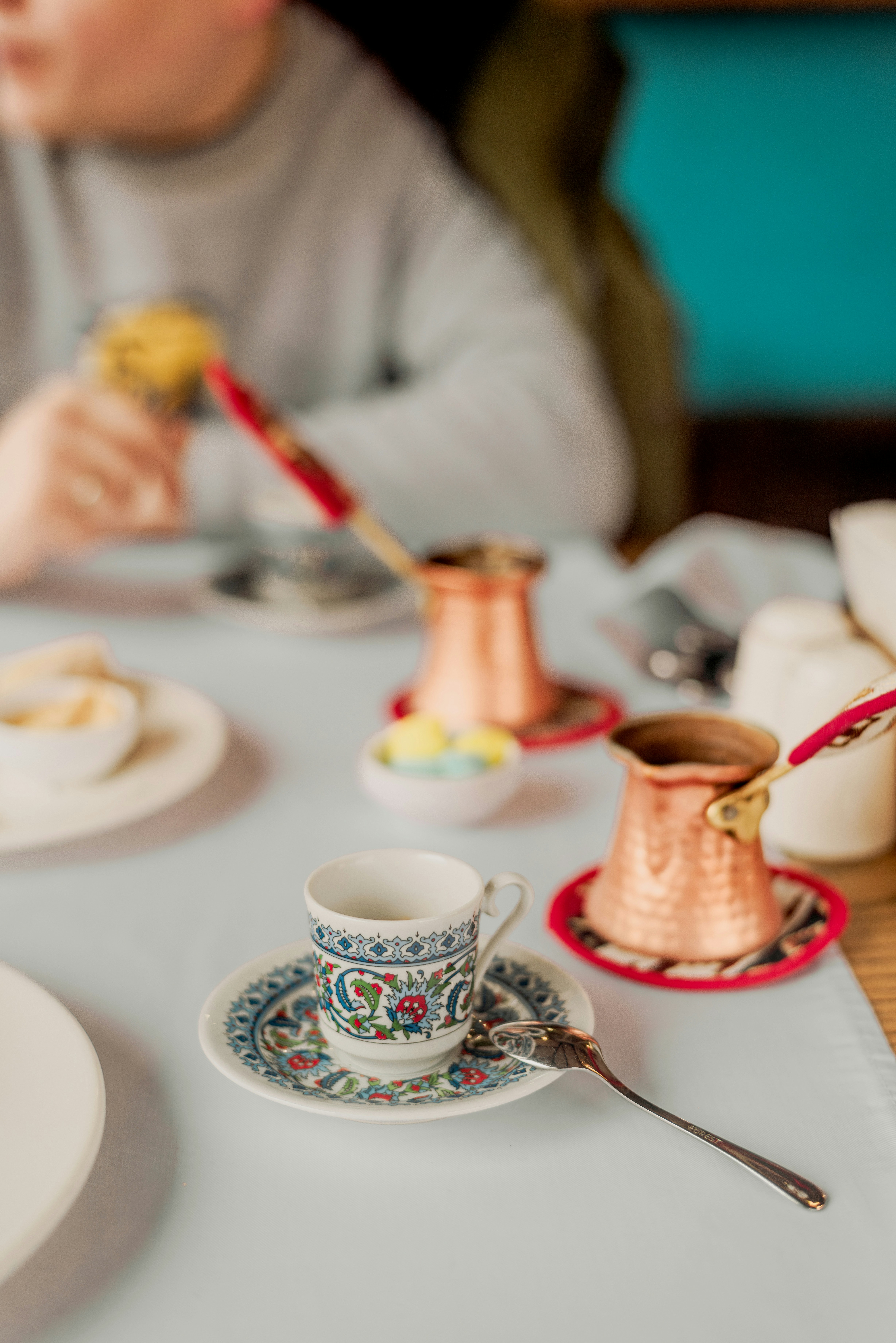 Teacup in Focus: Floral Pattern Framed by Copper Turkish Coffee Pots