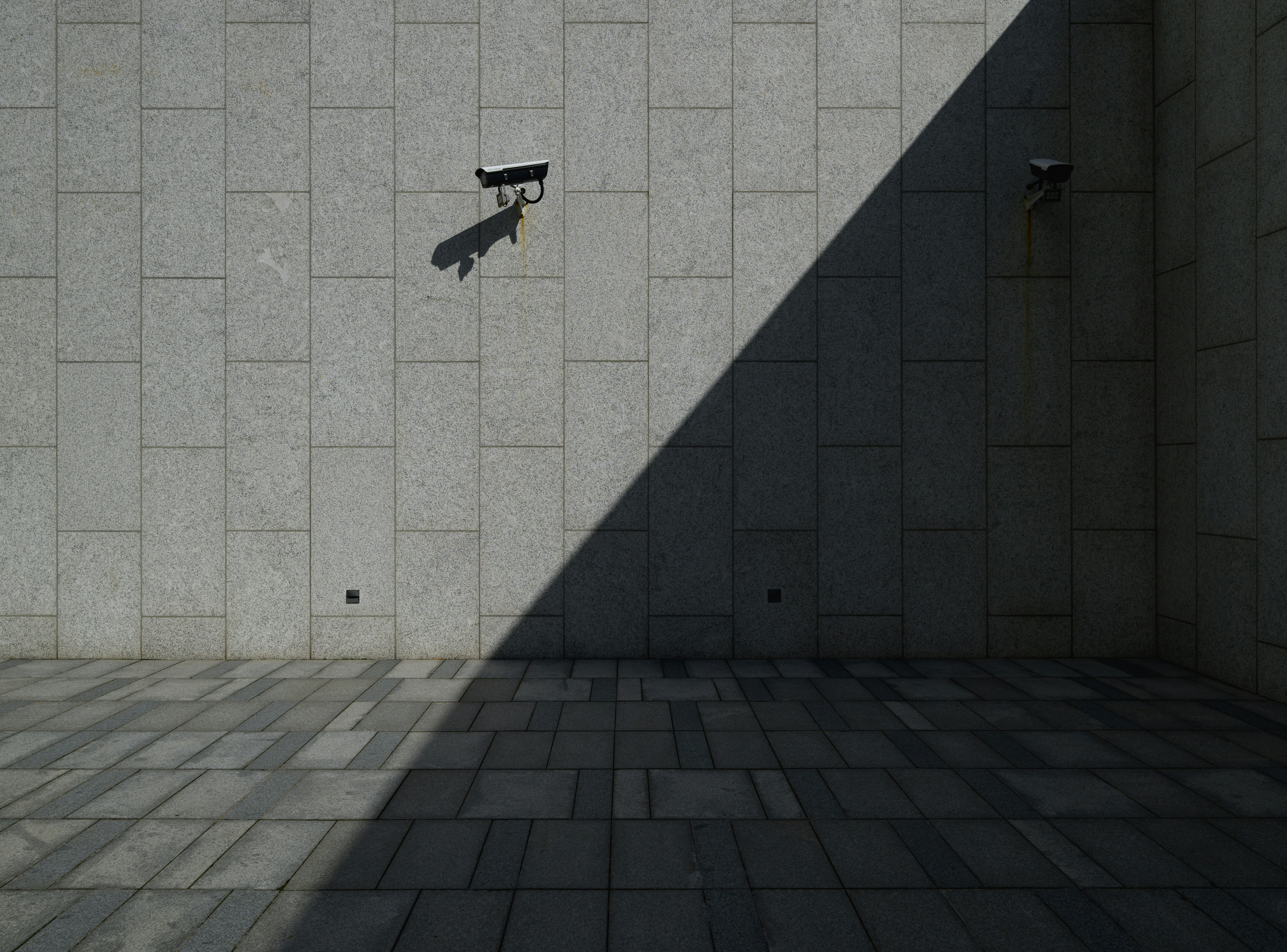 Angles of Vigilance: A Sunlit Wall Framed by Shadows and Dual Cameras