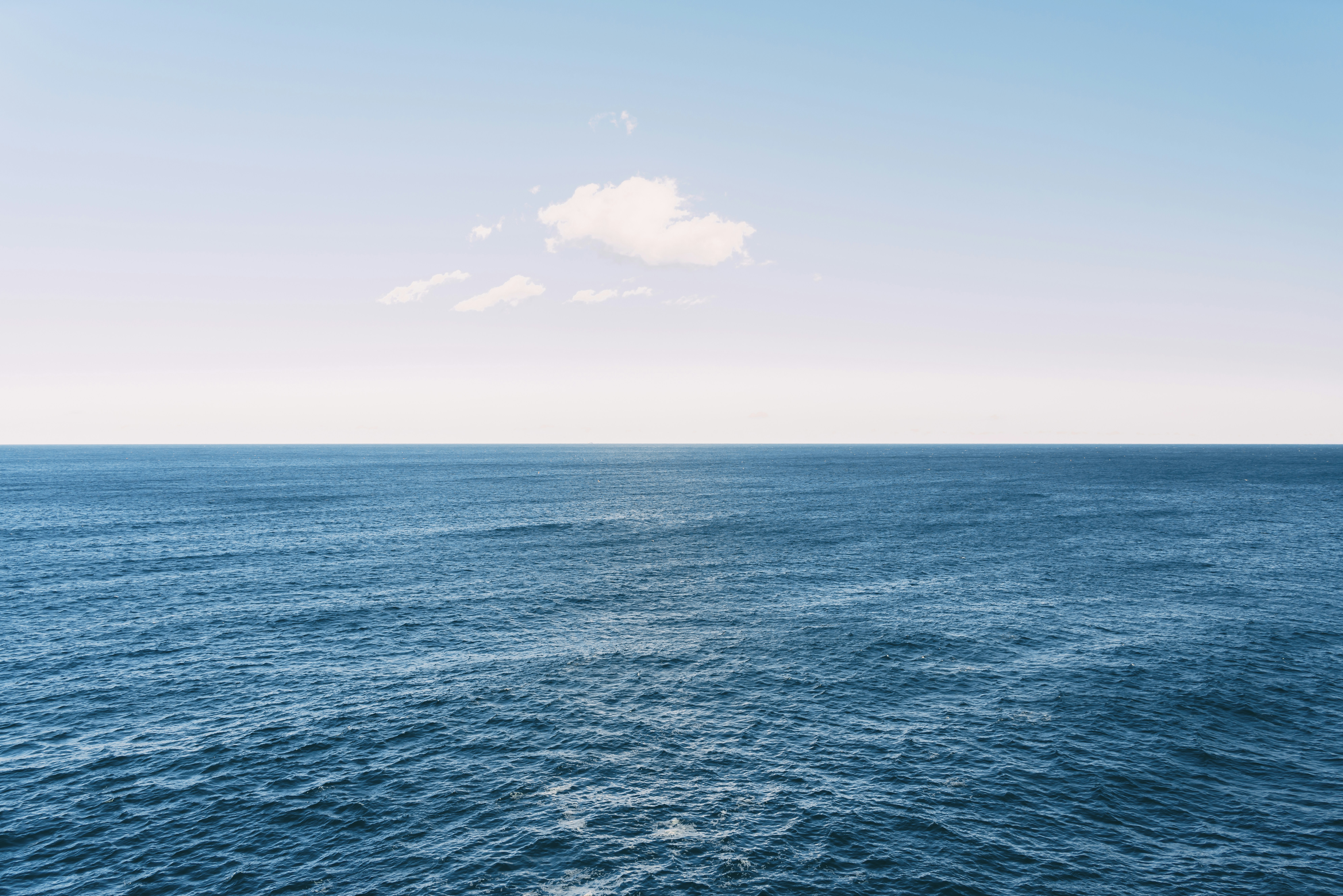 Vast ocean expanse under a serene sky, with gentle waves reflecting the soft light of a distant cloud.
