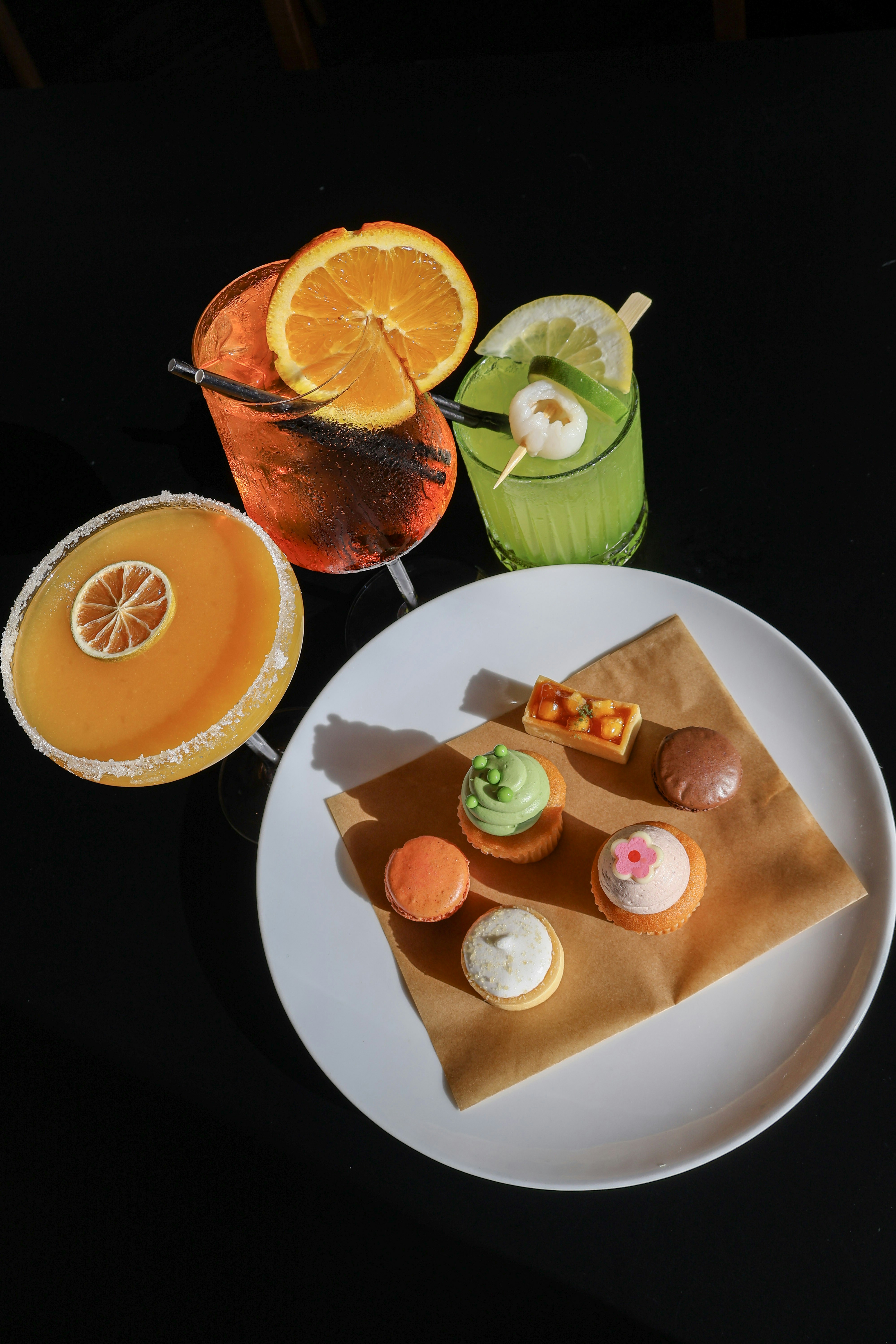 Citrus Confections at Night: Pastries and Colorful Cocktails on a Shadowed Table
