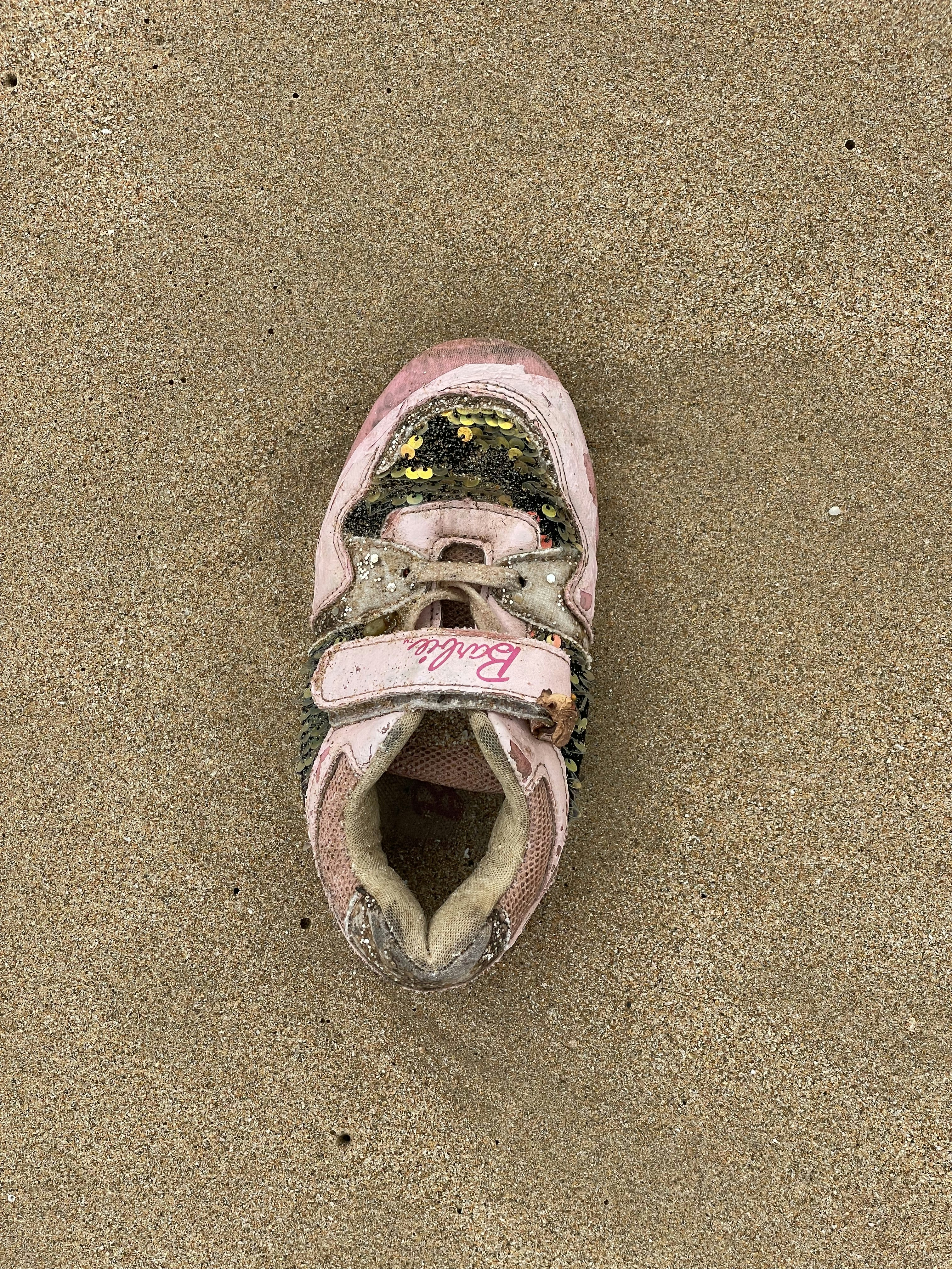 Pink Velcro Sneaker Resting on Damp Beach Sand, Weathered by the Tide
