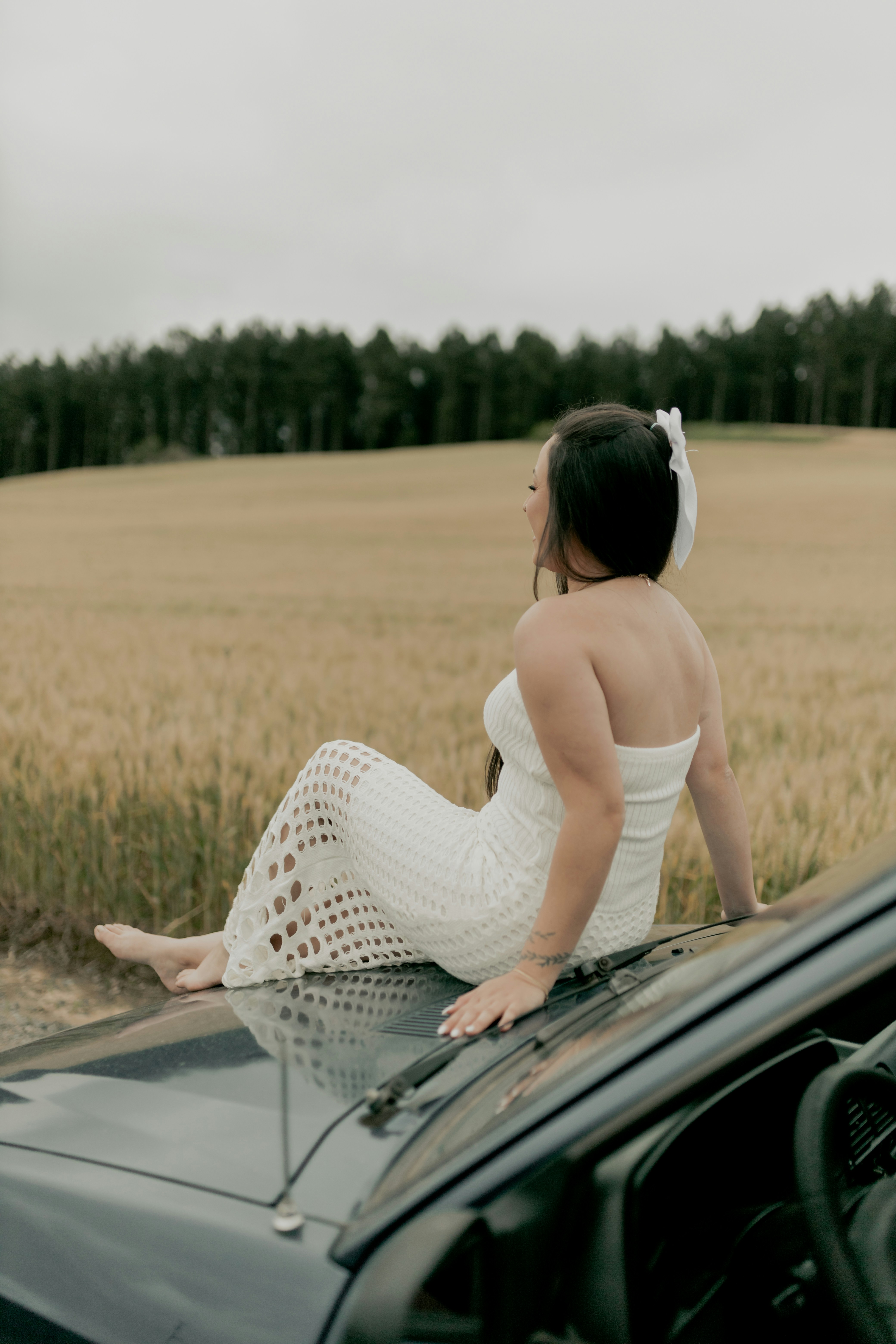 Midfield Reverie: A Woman in White Perched on a Car Hood Amid a Golden Field