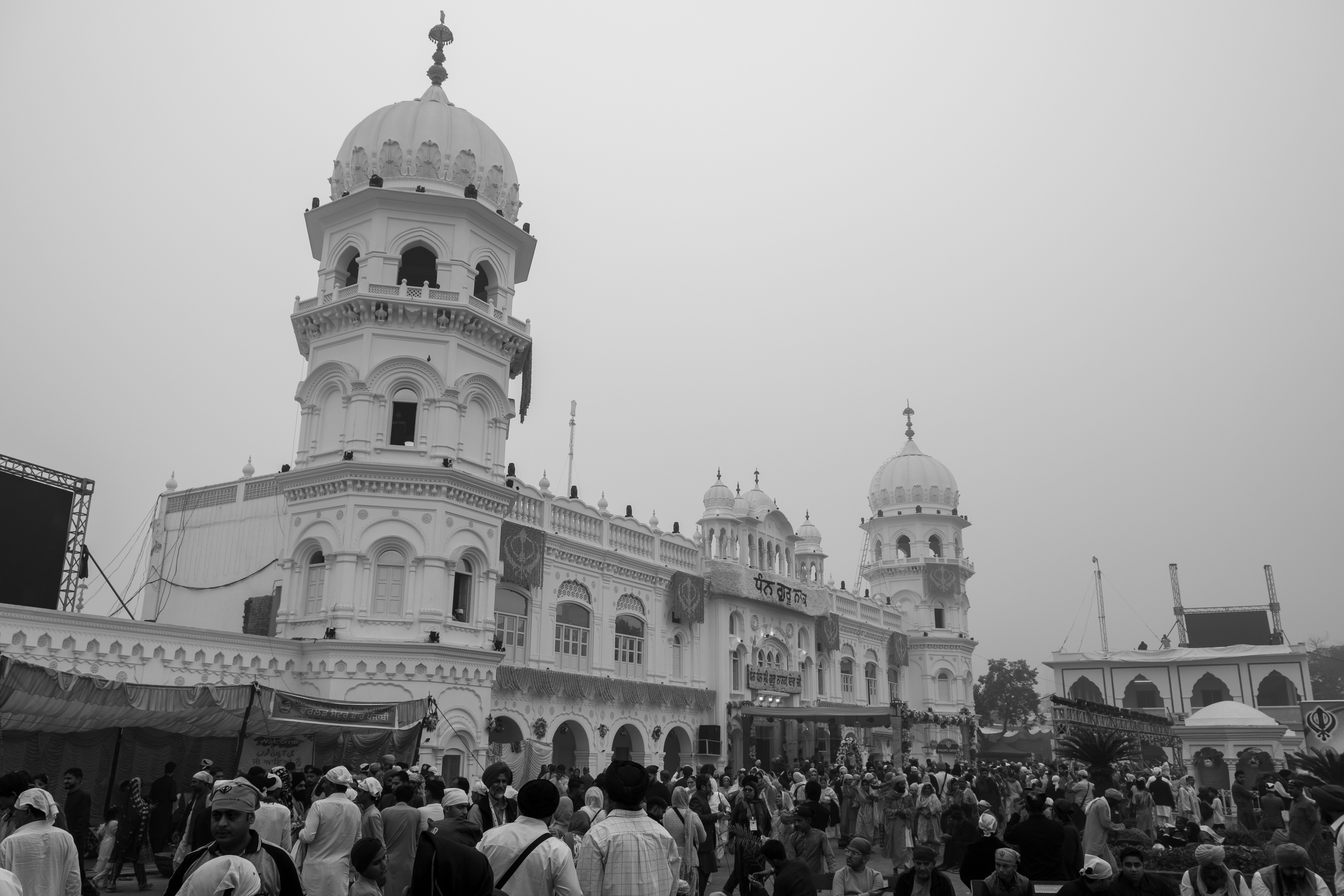Crowd of devotees outside the historic Nankana Sahib Gurudwara under an overcast sky.