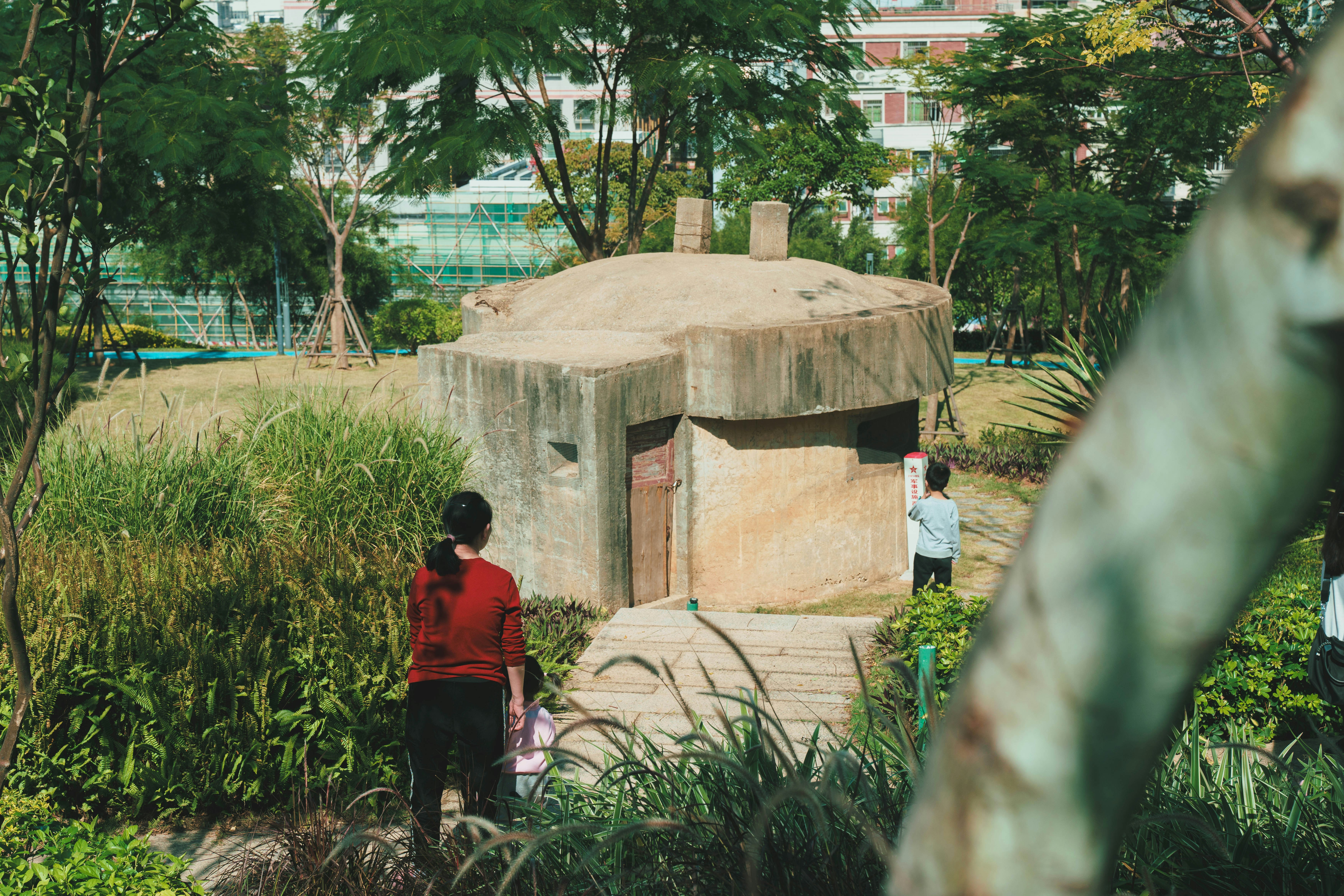 Concrete Shelter in a City Park, Framed by Greenery and Foot Traffic