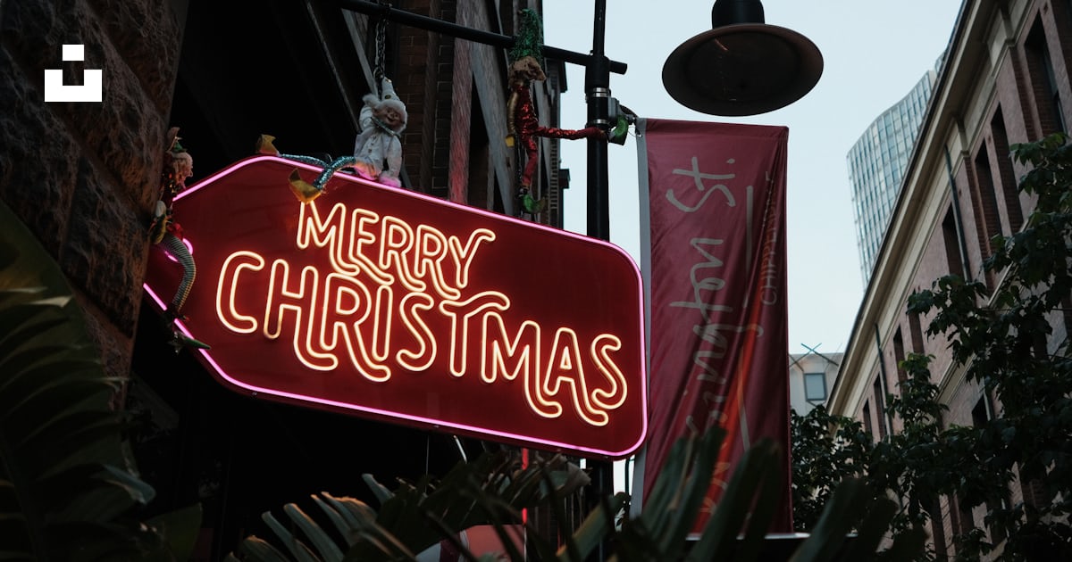 建物の側面からぶら下がっている赤いメリークリスマスの看板の写真 Unsplashのクリスマスの無料画像