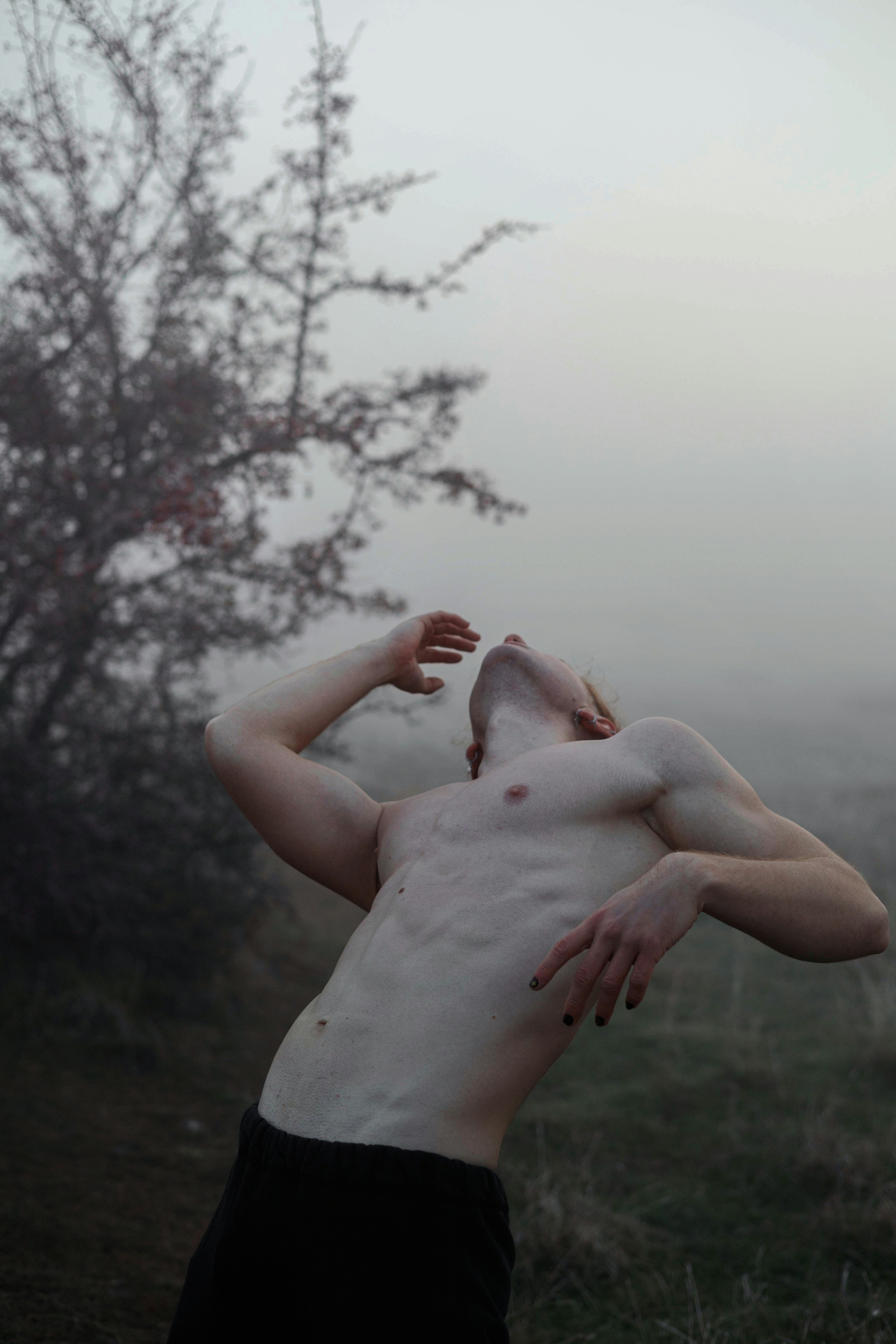 Mistbound Reach: A shirtless silhouette defying the fog on a windswept hillside