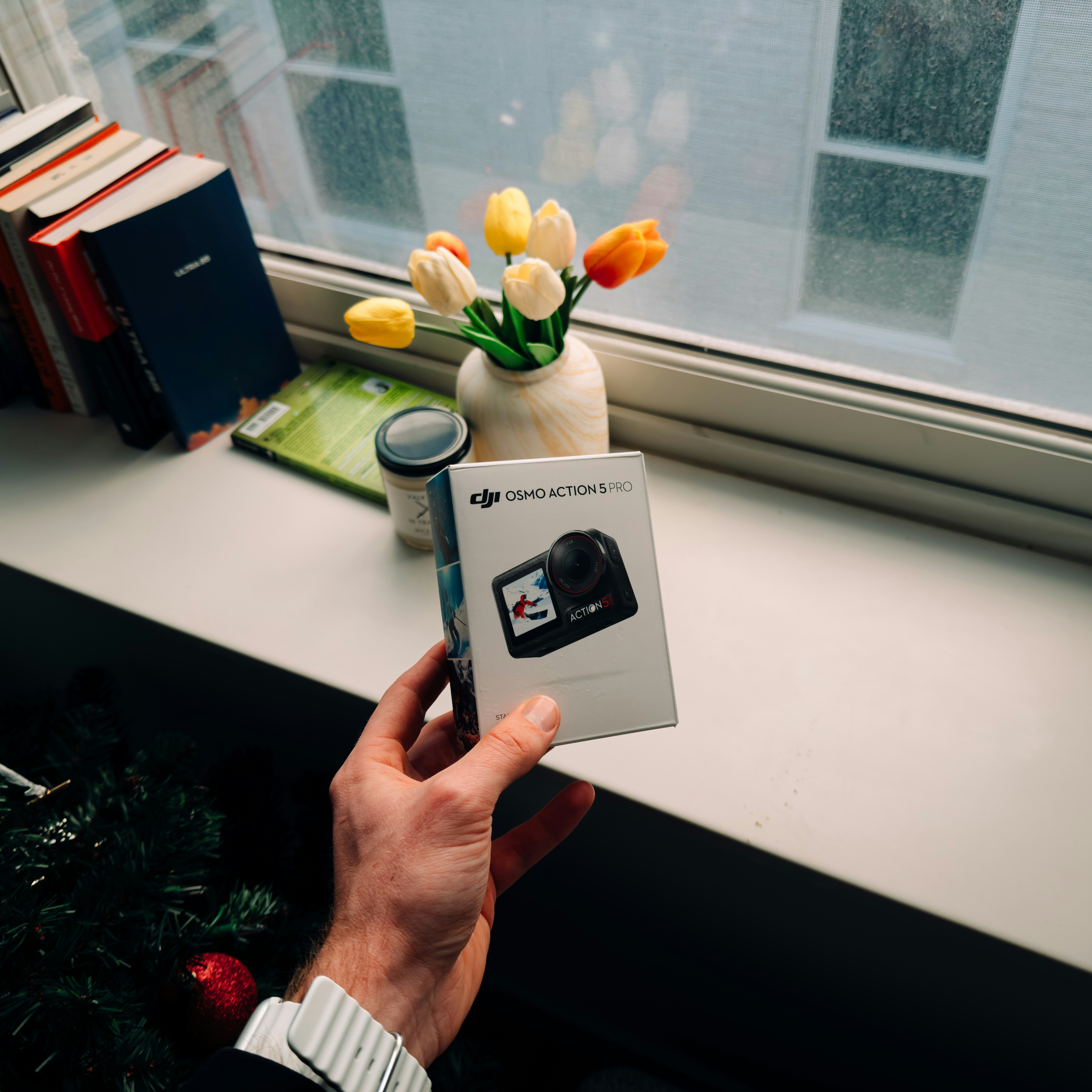 Unboxing the Osmo Action 5 on a sunlit windowsill among tulips and books