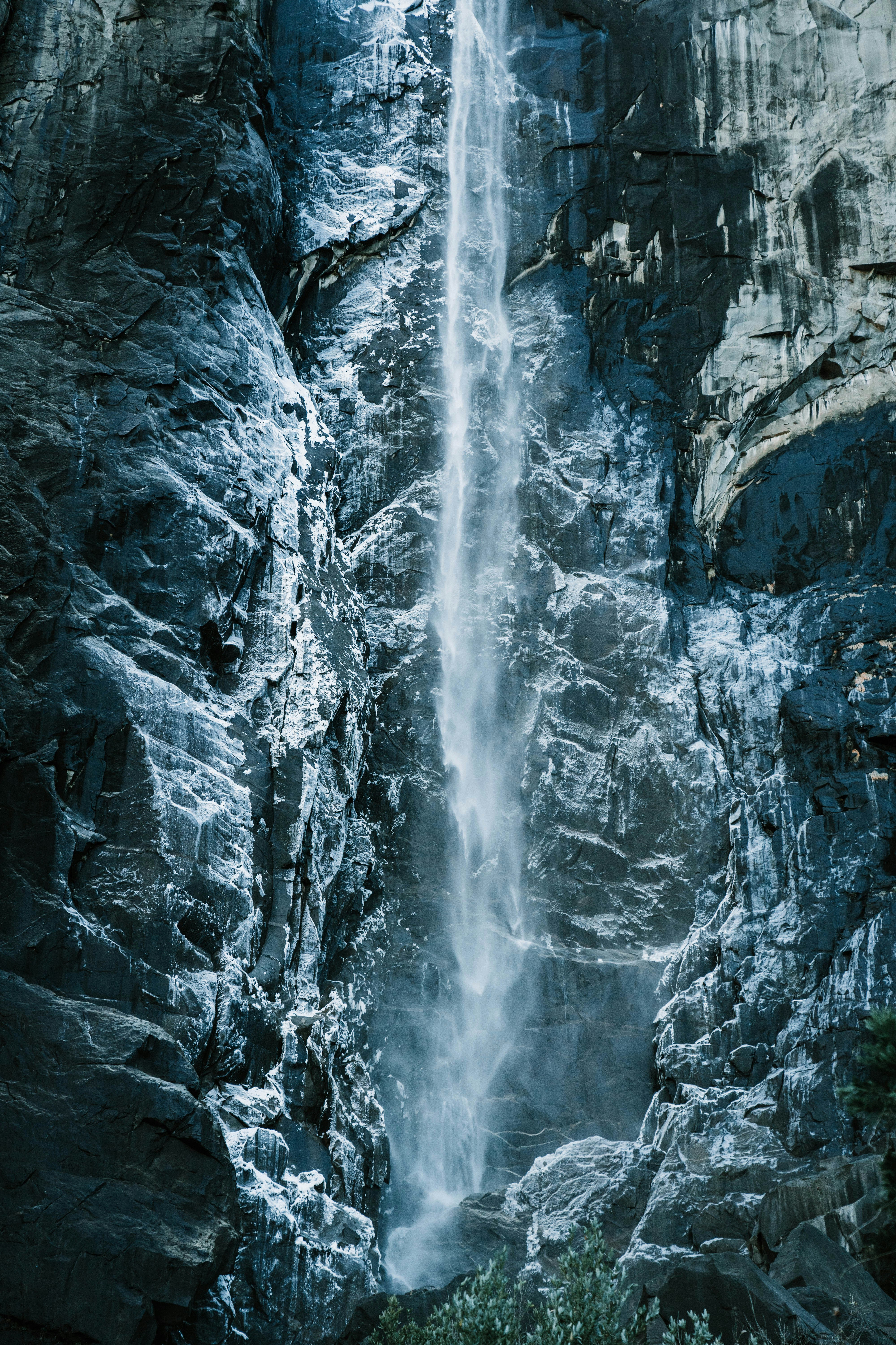 Waterfall descends rugged dark cliffs, with soft mist rising, creating a mystical atmosphere.