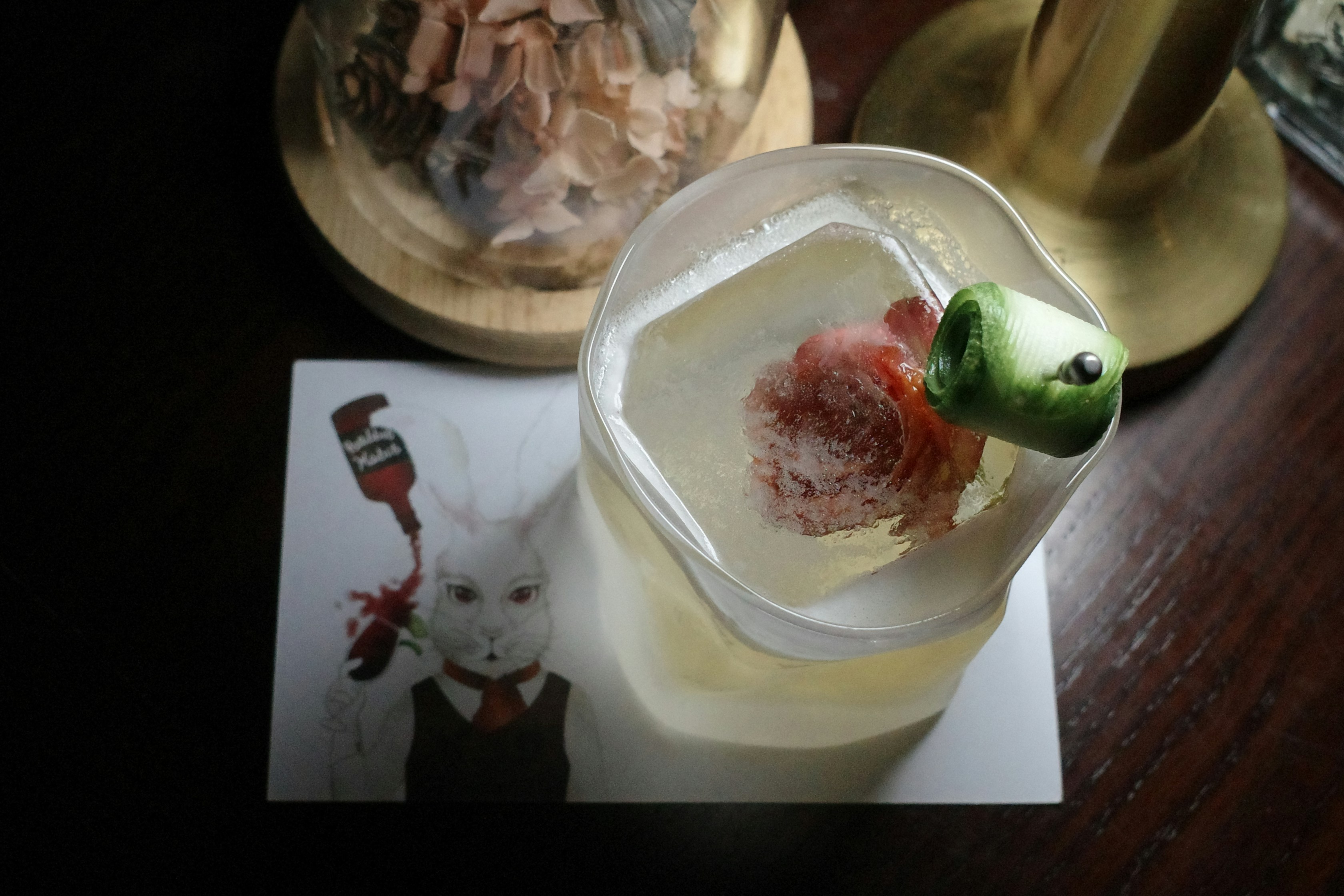 Citrus Glisten: a cucumber-garnished cocktail on a cat-illustrated napkin