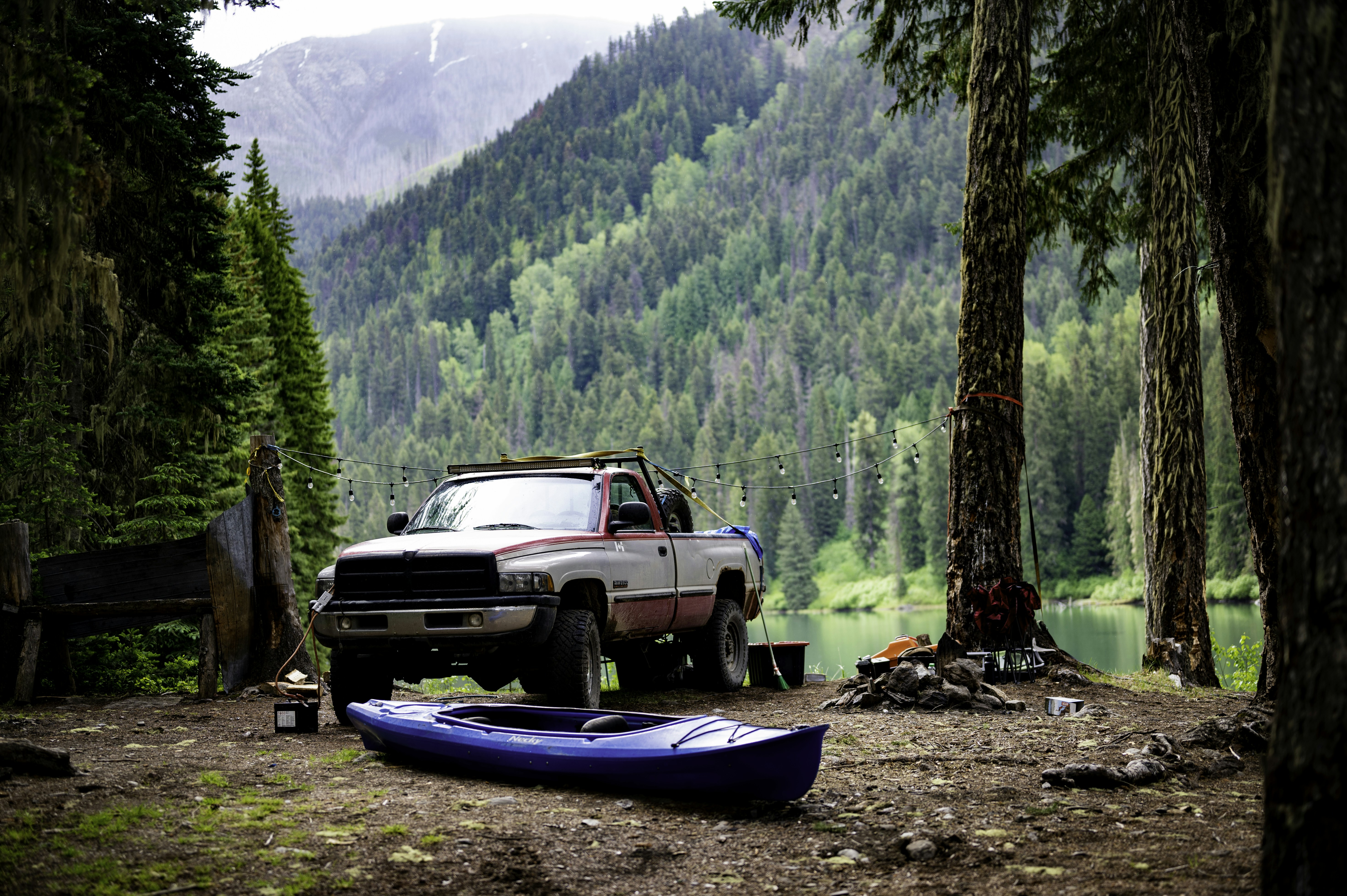 Lakeside Stopover: A Blue Kayak, a Red-Trim Truck, and Silent Pines