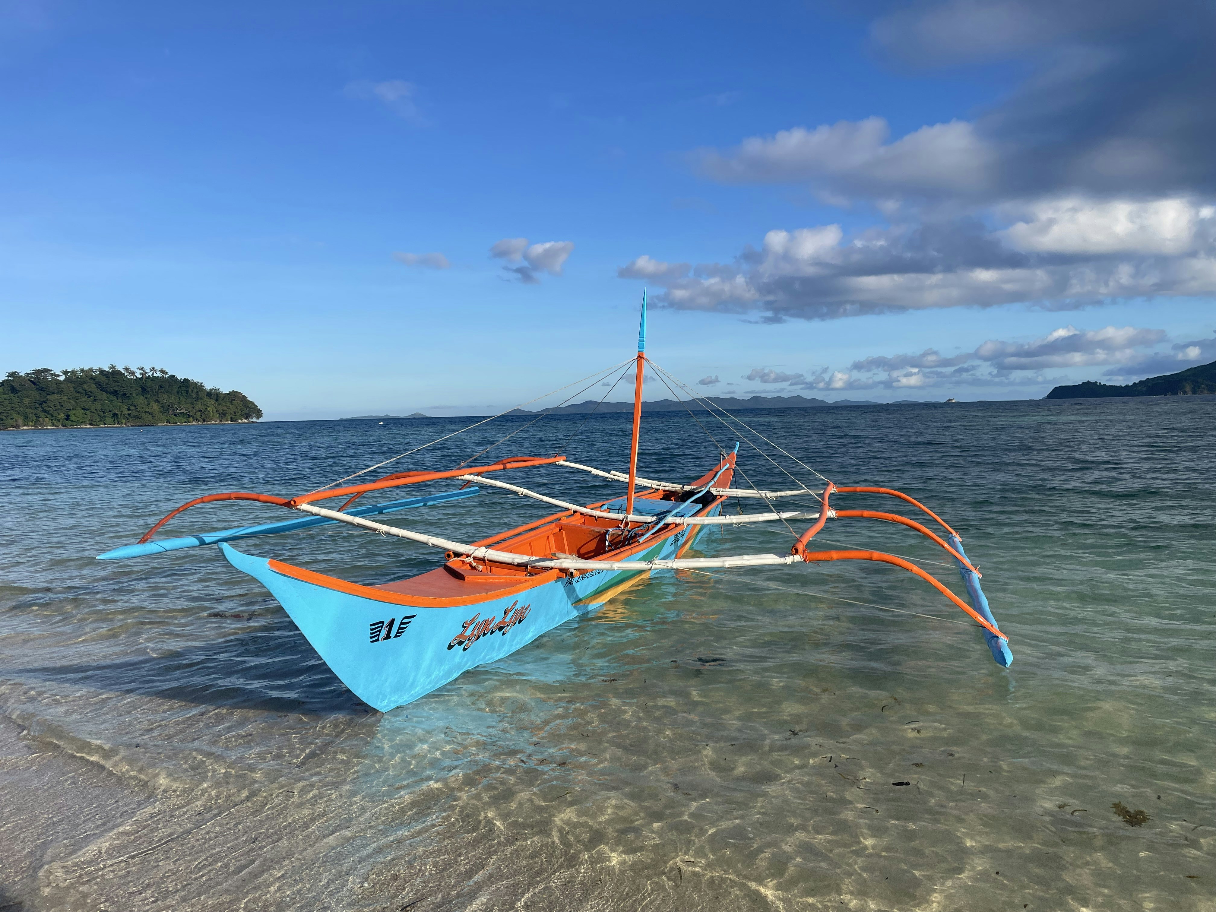 Turquoise Shoreline: A Blue Outrigger with Orange Rigging