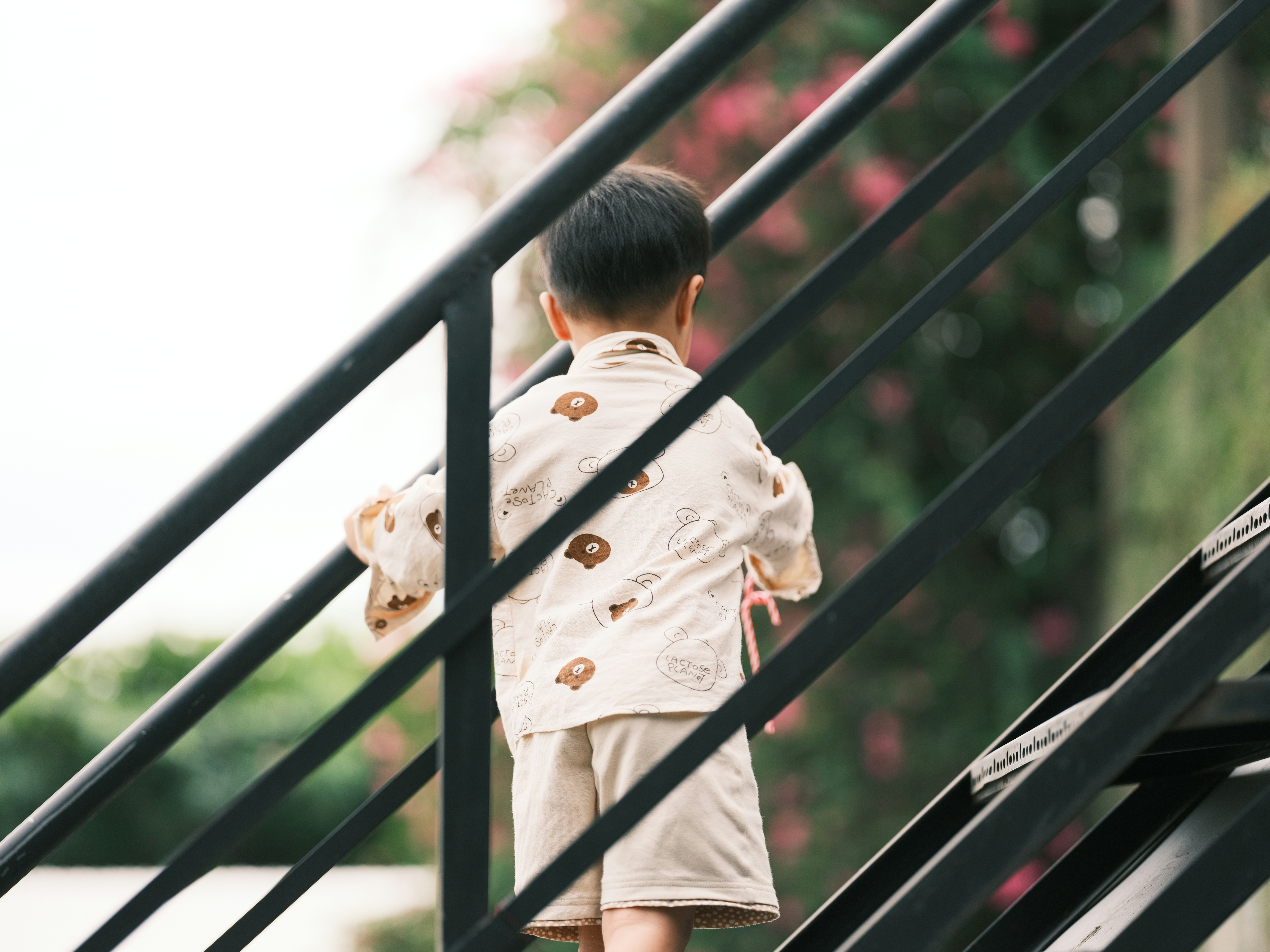 Child ascending metal stairs surrounded by greenery and flowers.