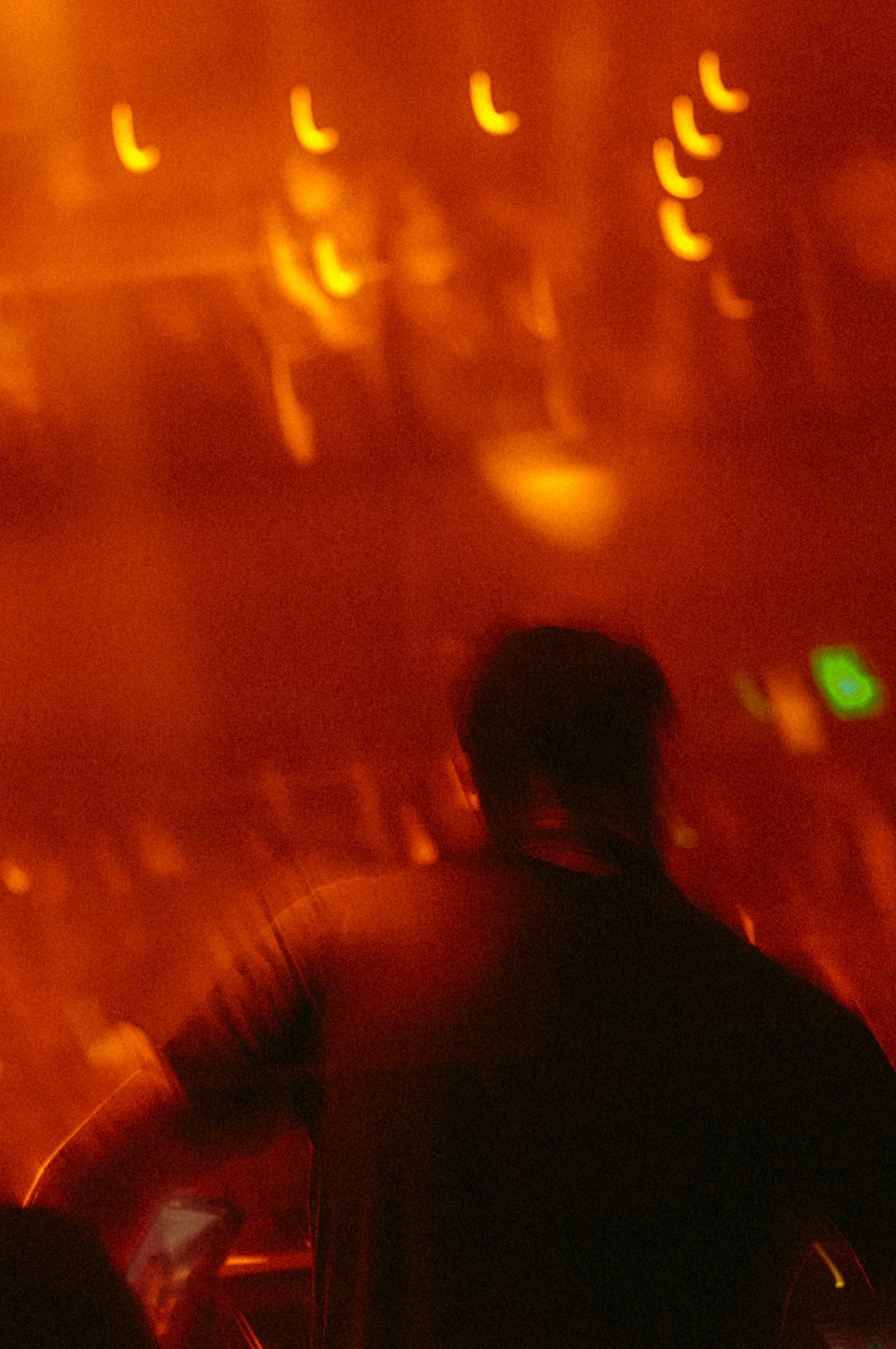 Silhouette of a DJ immersed in vibrant orange light at a lively event, surrounded by energetic crowd movements.