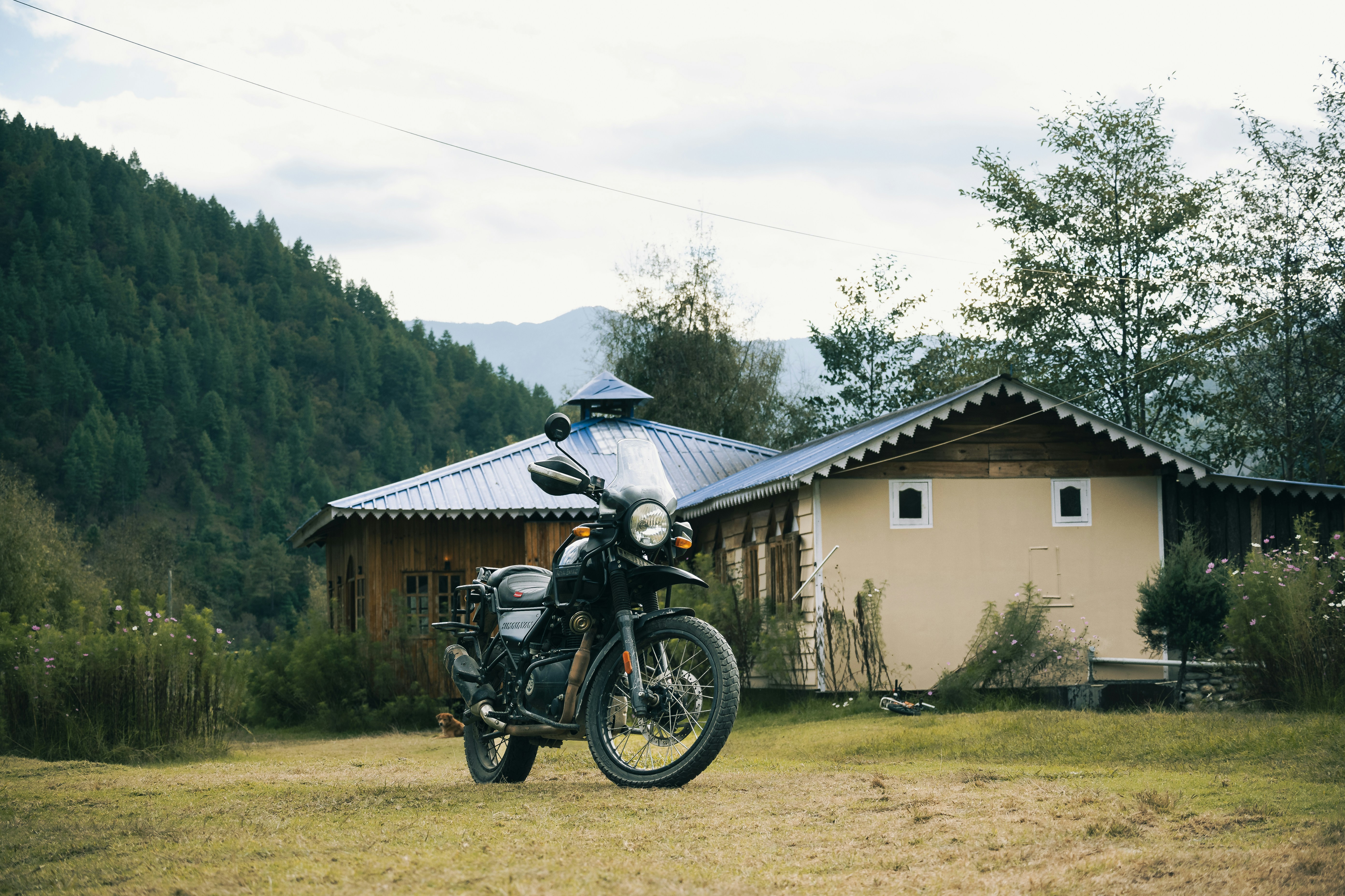 Vintage motorcycle by a rustic hillside cabin as forested slopes loom