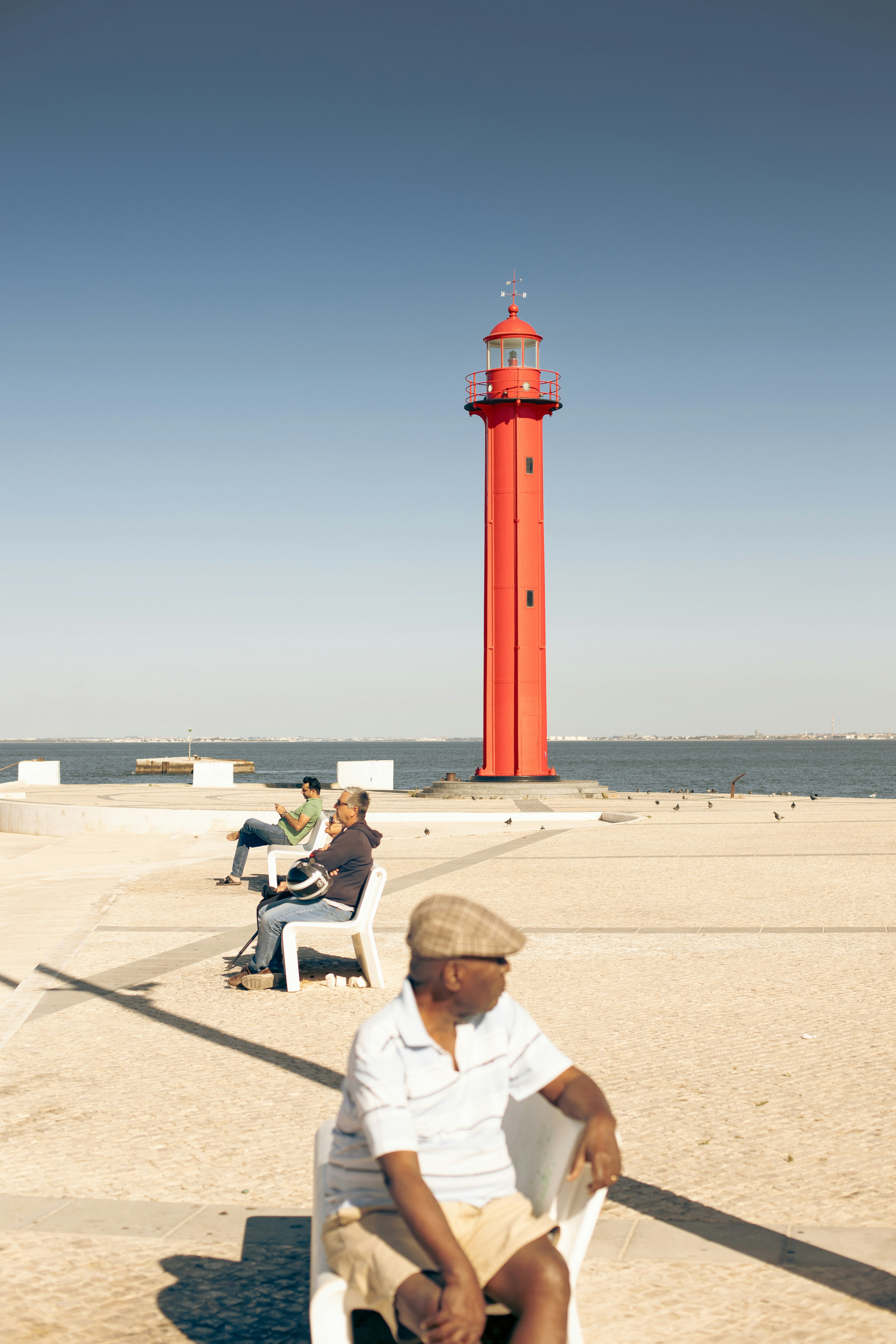 Red Lighthouse at Sunset Beach with Seated Onlookers