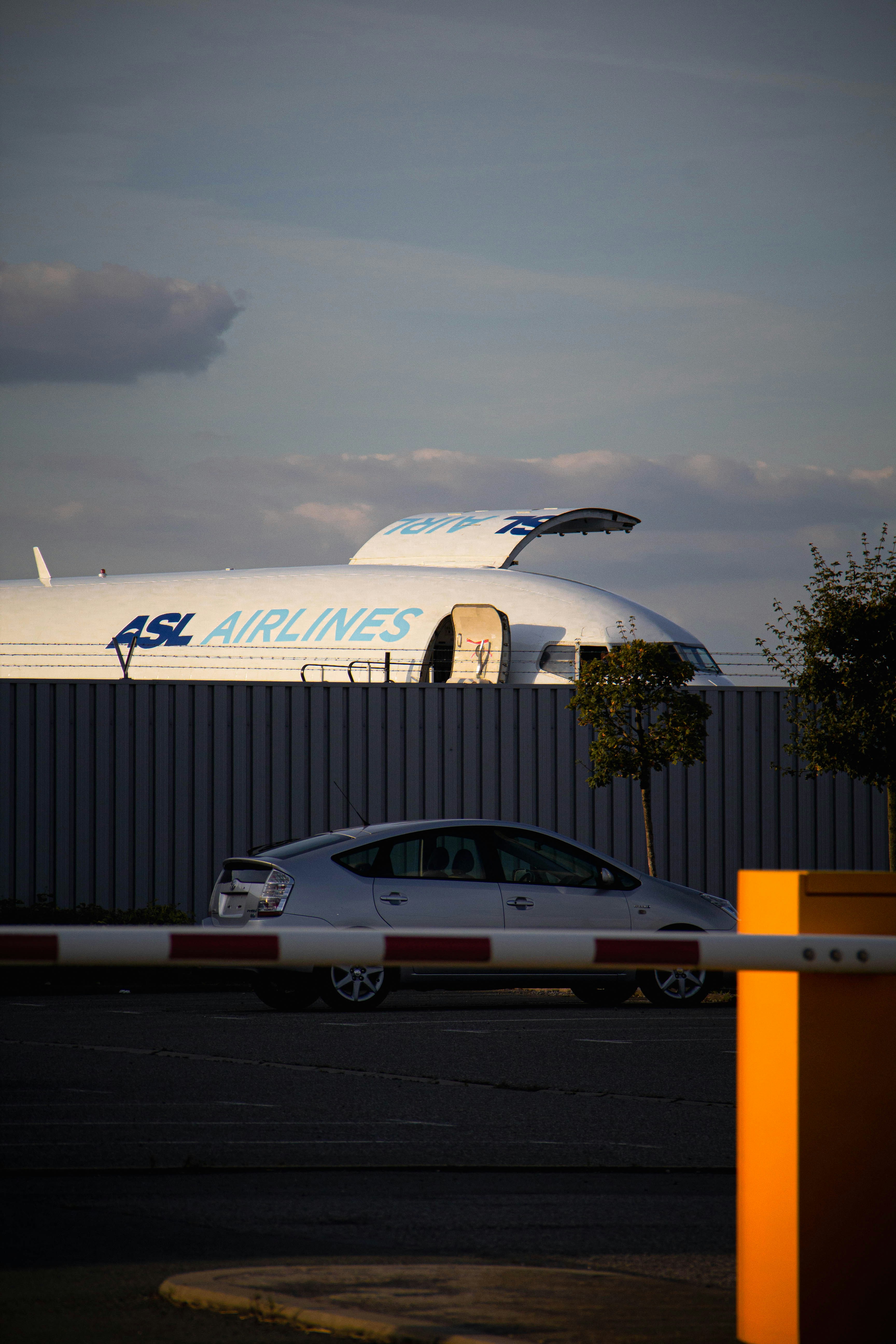 Blue-and-White Jet Shrouded by Aisle of Fence and Car